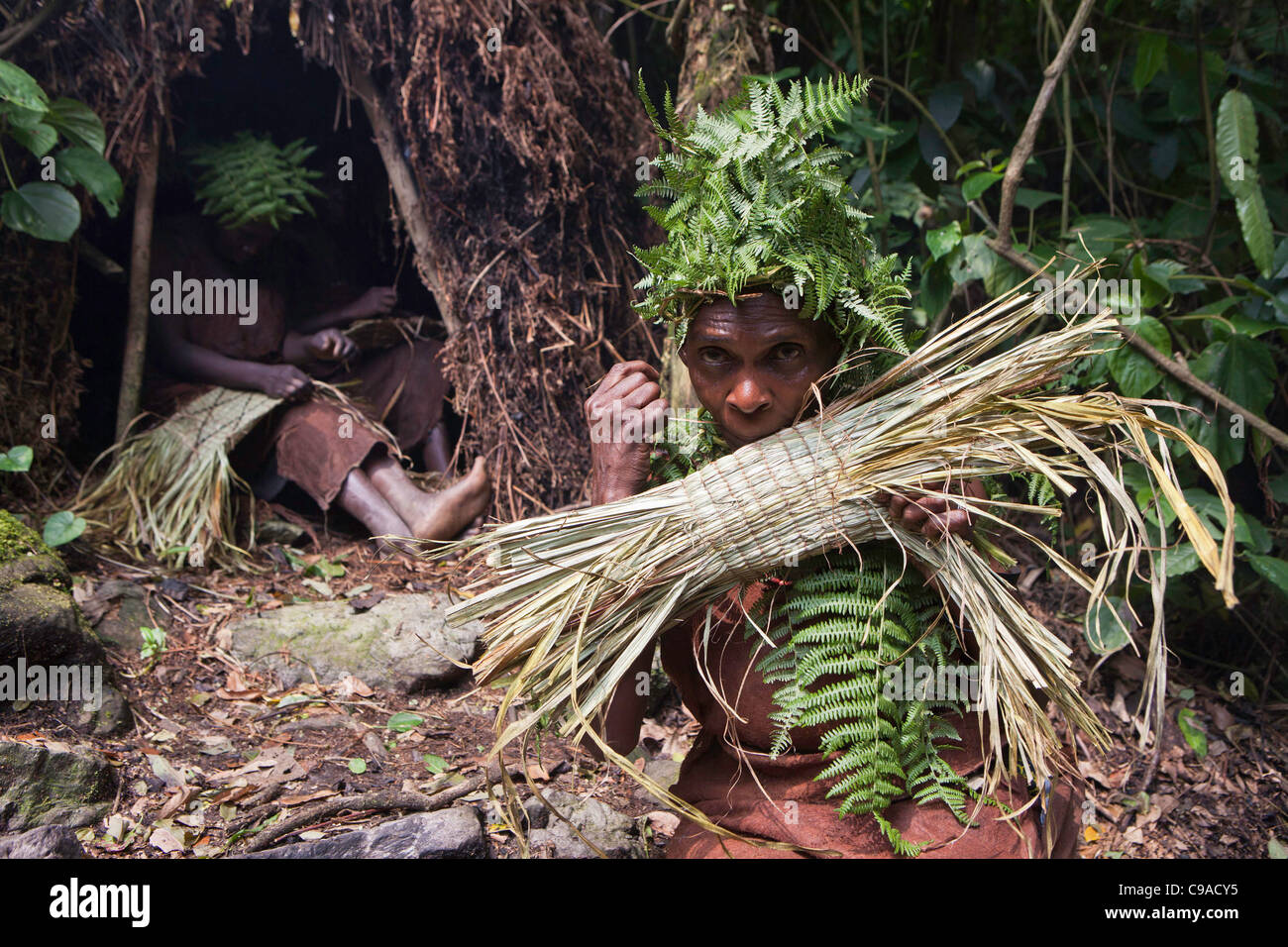 Batwa woman in traditional dress uses reeds to make a basket. Batwa ...