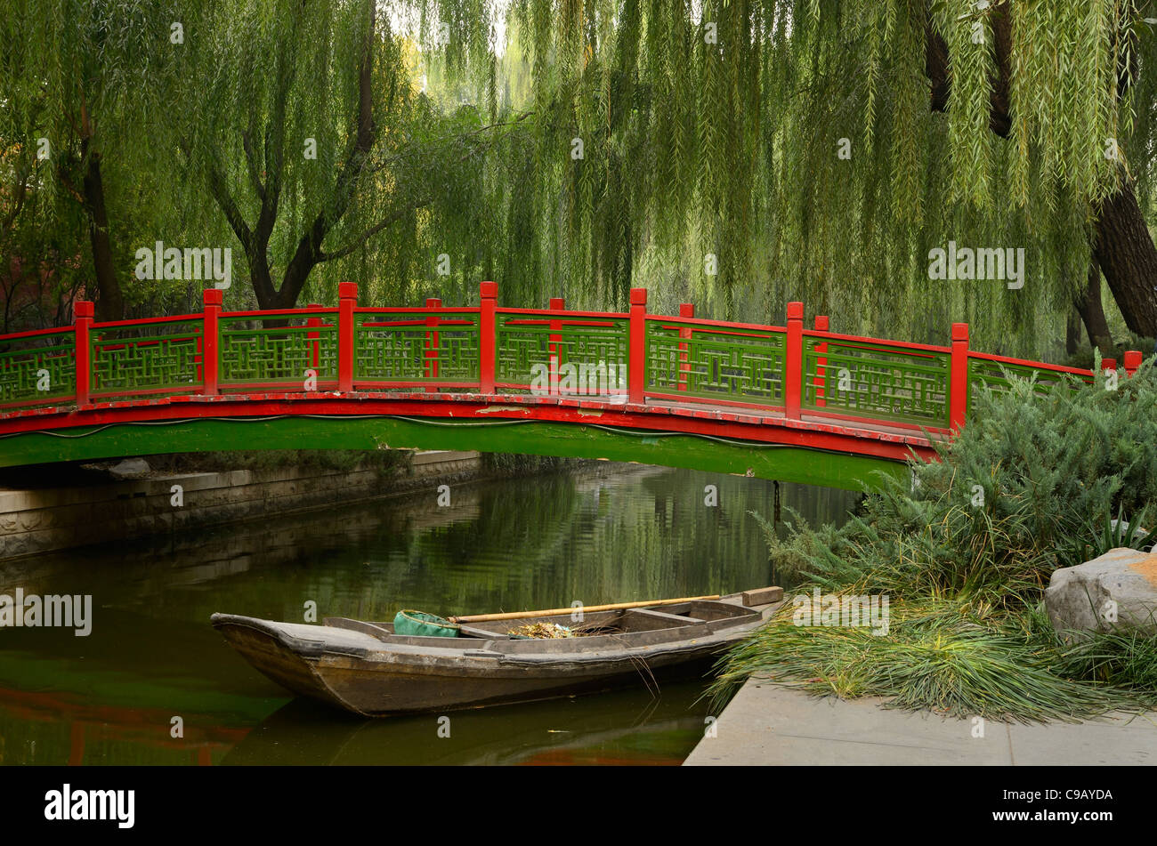 Old bridge with red railing and boat with green drooping willow tree ...