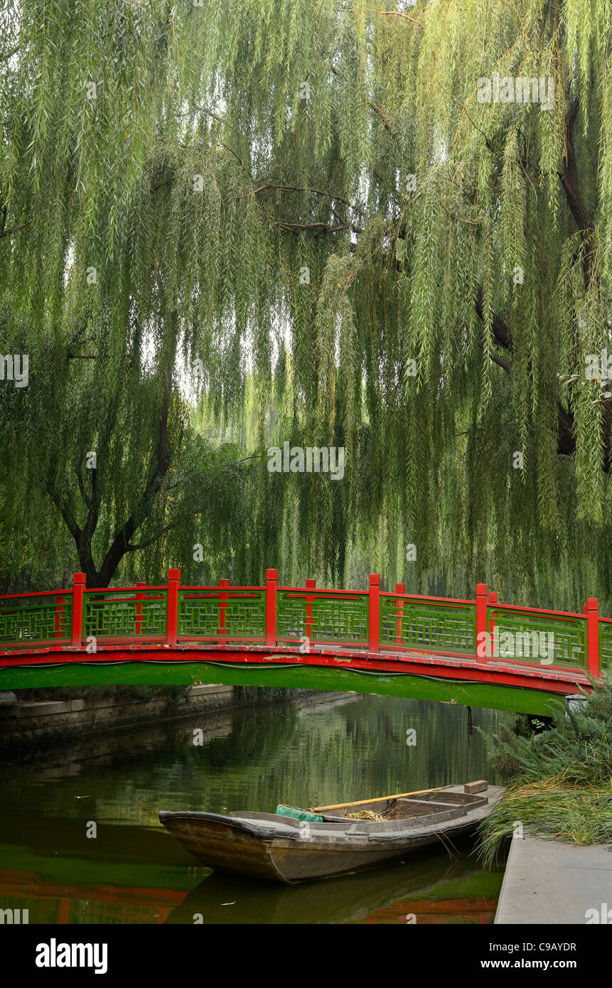 Old bridge with red railing and boat with green drooping willow tree ...