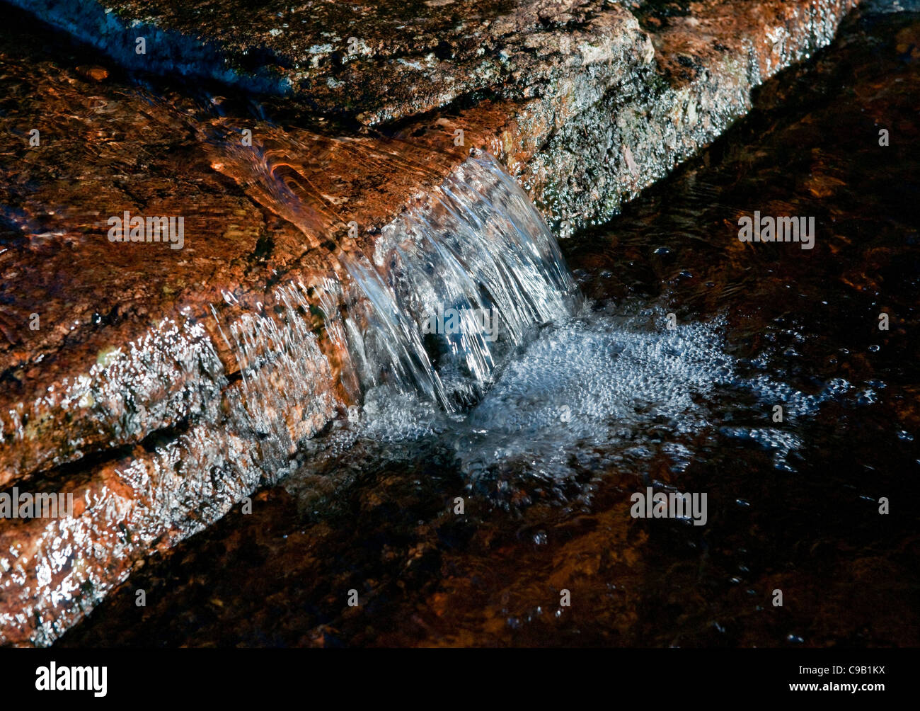 River water flowing over a small rock ledge making bubbles as it lands ...