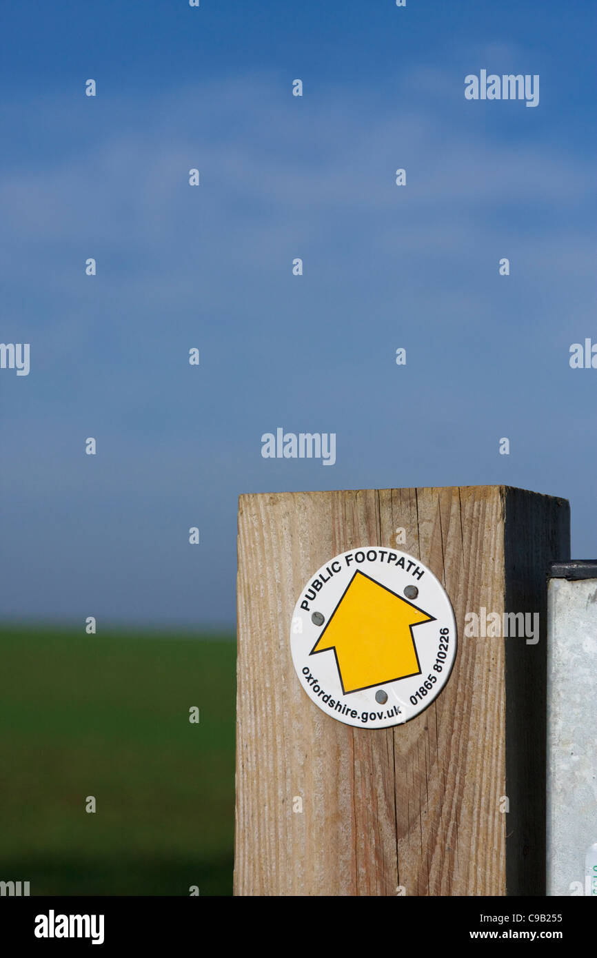 Circular public footpath sign mounted on wooden post. Blue sky with ...