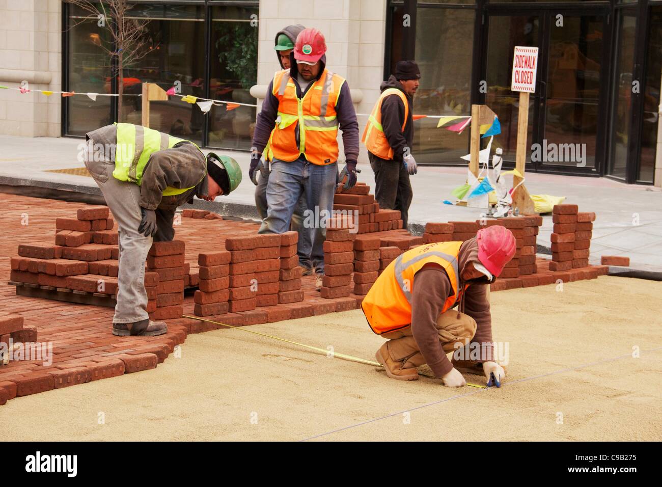Construction workers take a measurement before laying paving bricks ...