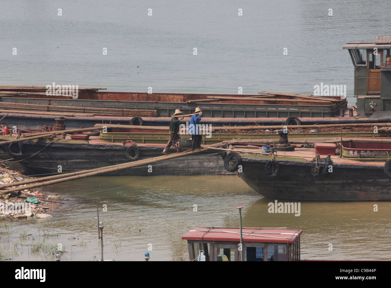 Two men using a carying pole to load junk onto a barge at Chizhou ...