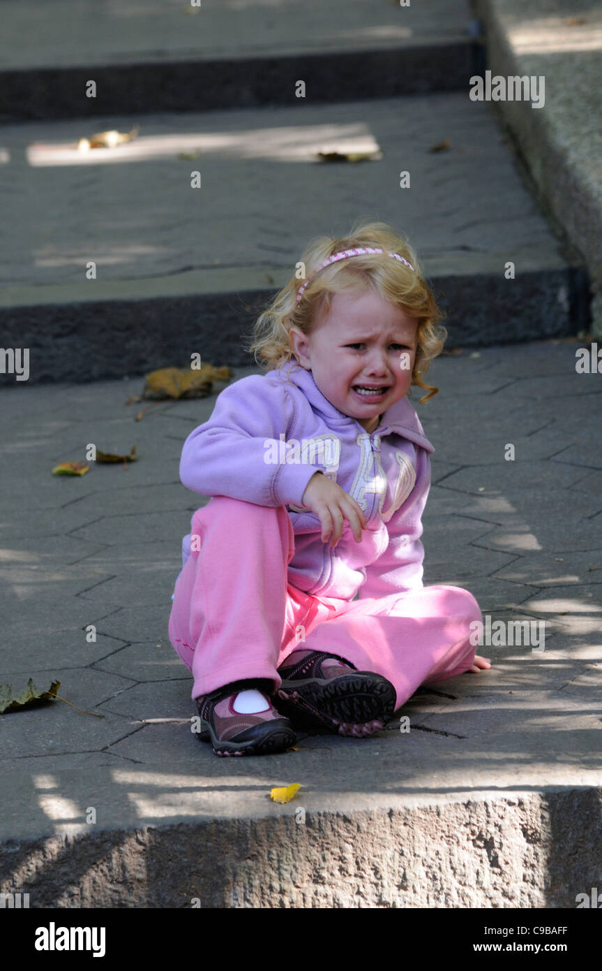 Little girl sitting on the ground and crying having fallen or tripped ...