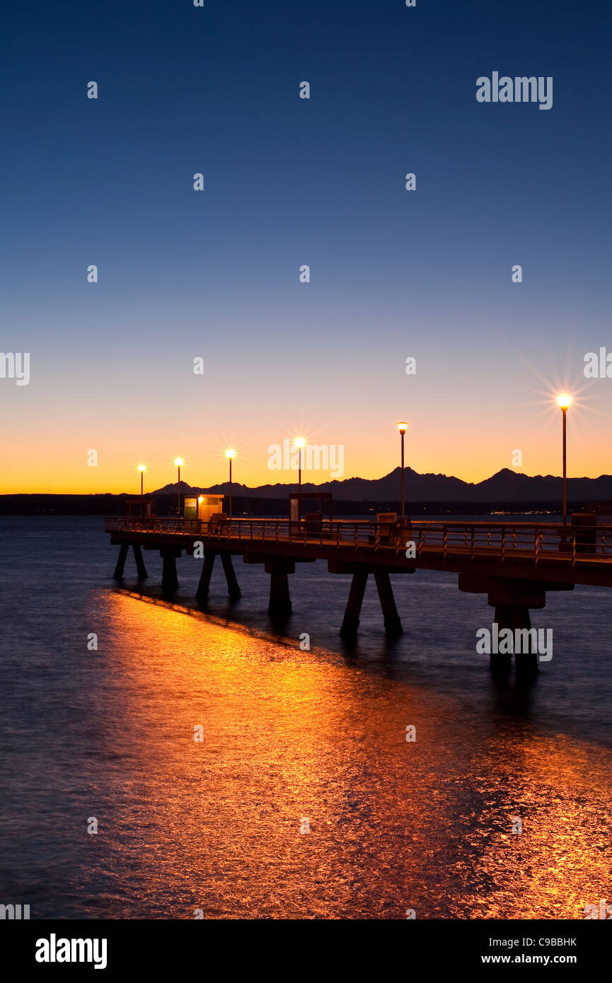 Silhouetted pier with people fishing off dock at sunset on Puget Sound ...