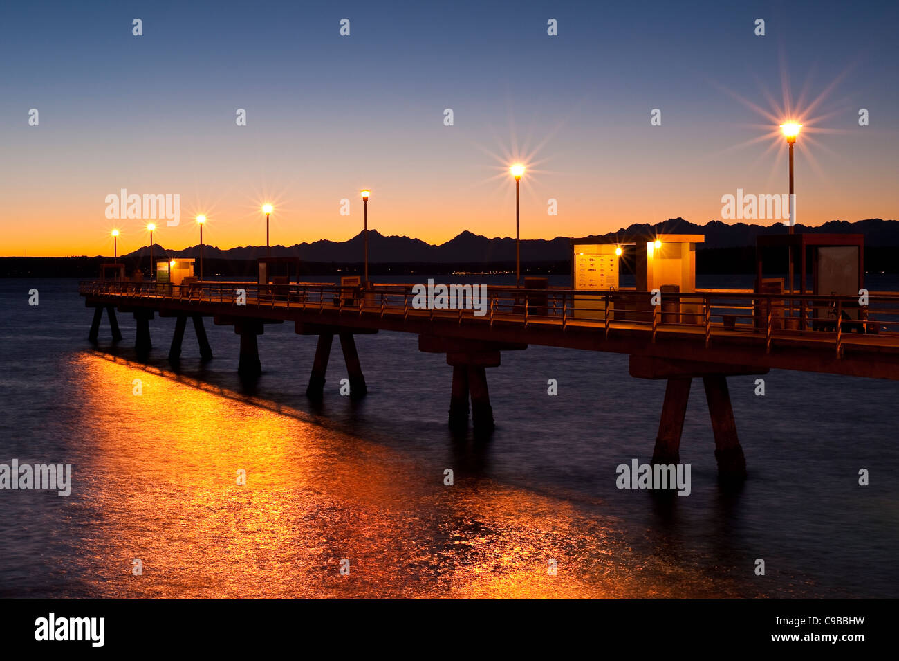 Silhouetted pier with people fishing off dock at sunset on Puget Sound ...