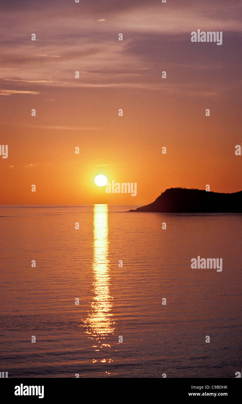 Scenic landscape of sunset over a calm ocean with a mountain silhouette ...