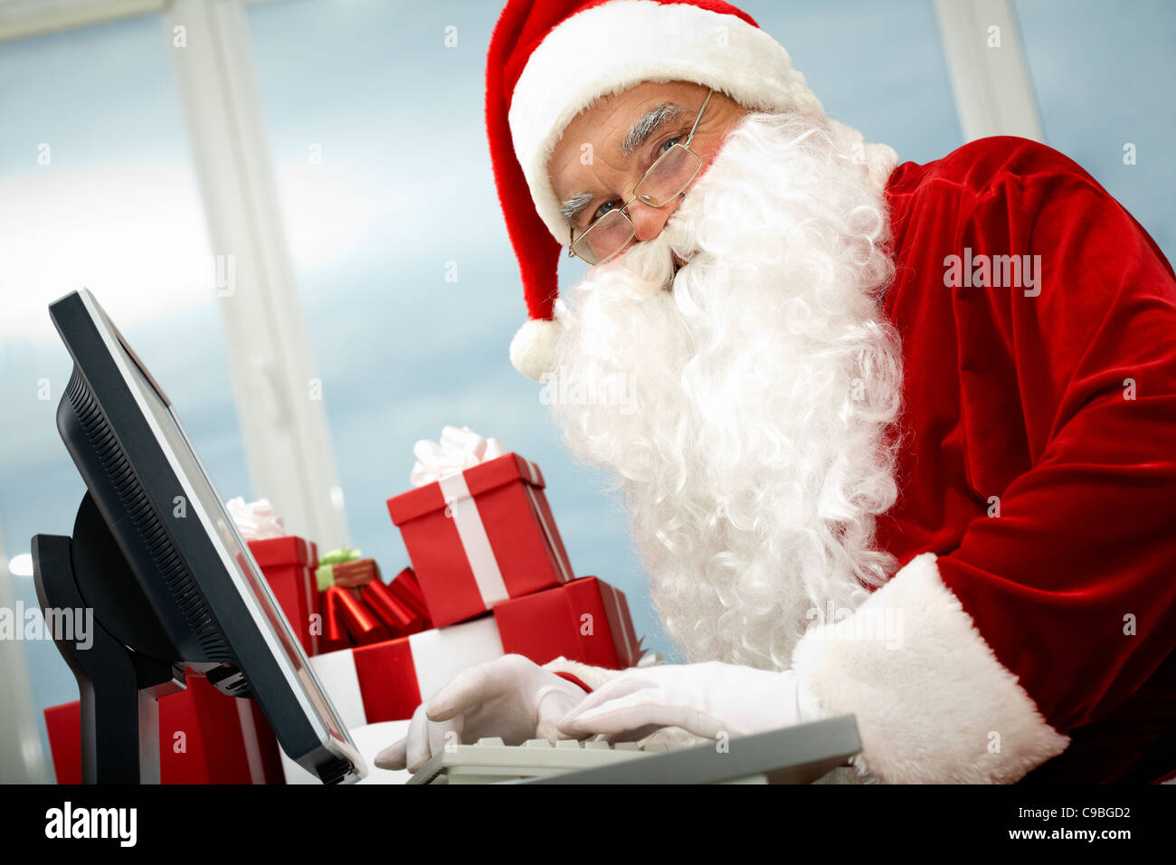 Portrait of Santa Claus in front of computer monitor looking at camera ...