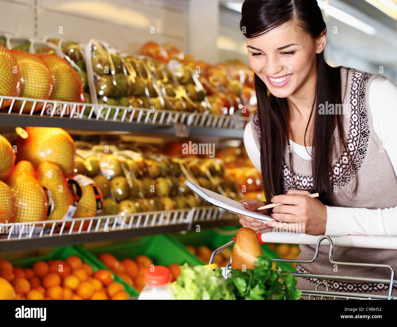 Image of pretty woman choosing products in supermarket with list of ...