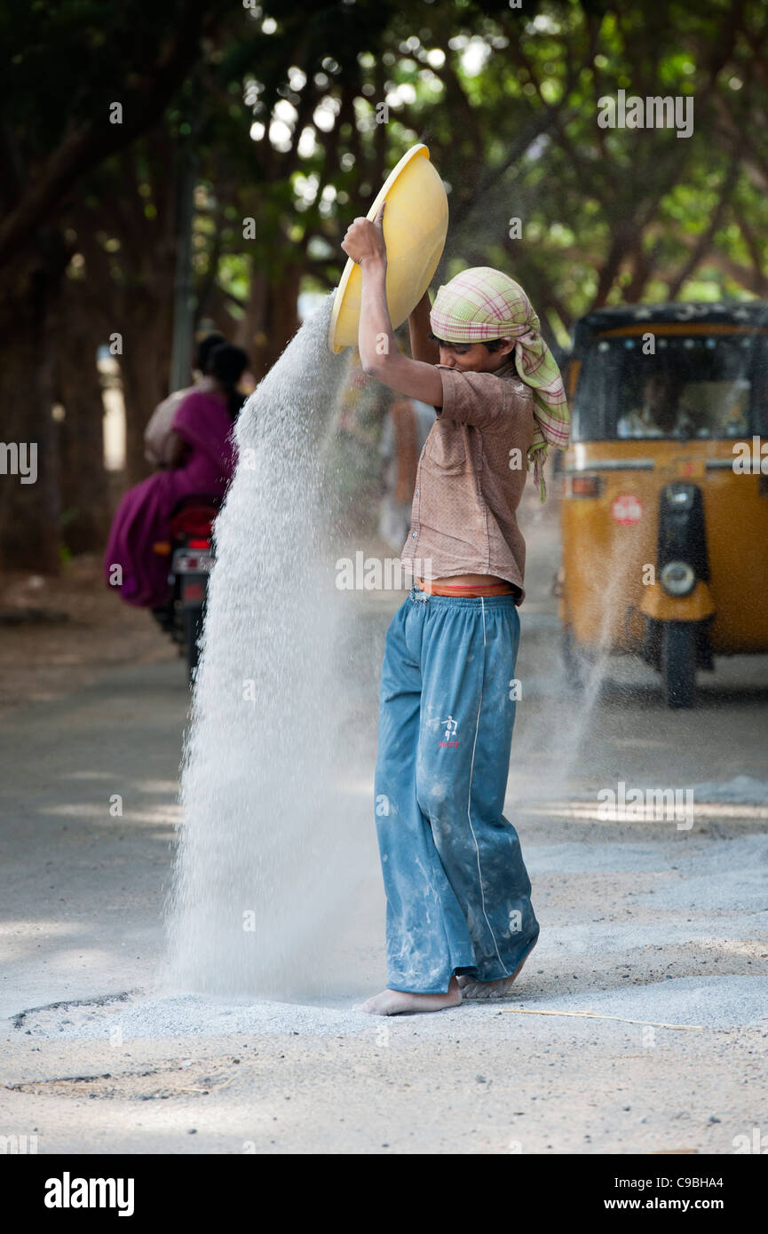 Road working indian boy filling in potholes with fine crushed stone ...