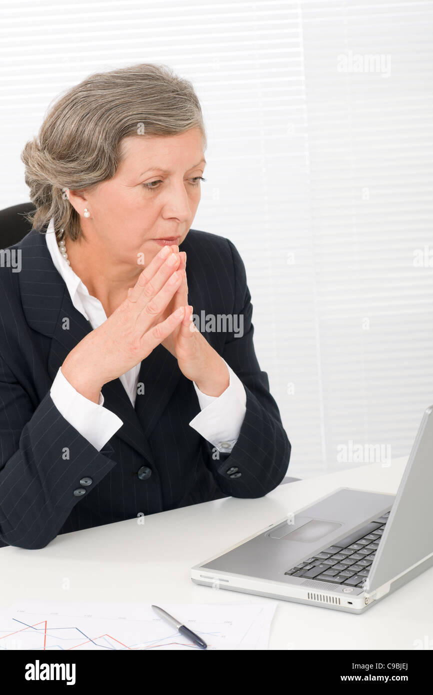 Senior businesswoman looking seriously at computer sitting behind ...
