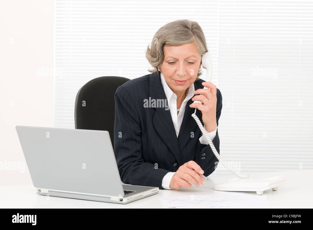Serious successful senior businesswoman sitting behind office table ...