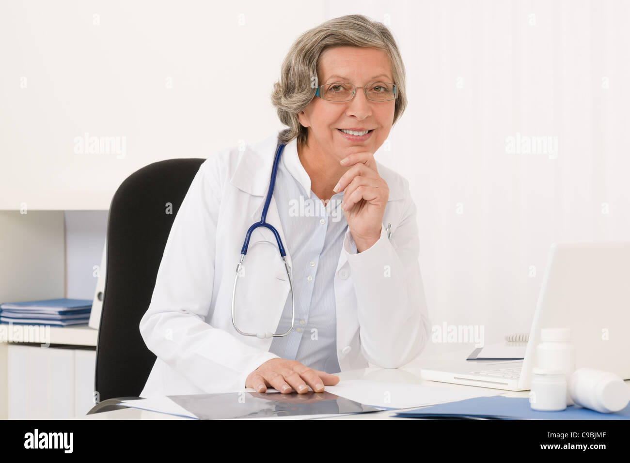 Doctor office - senior female physician sit behind desk smiling Stock ...