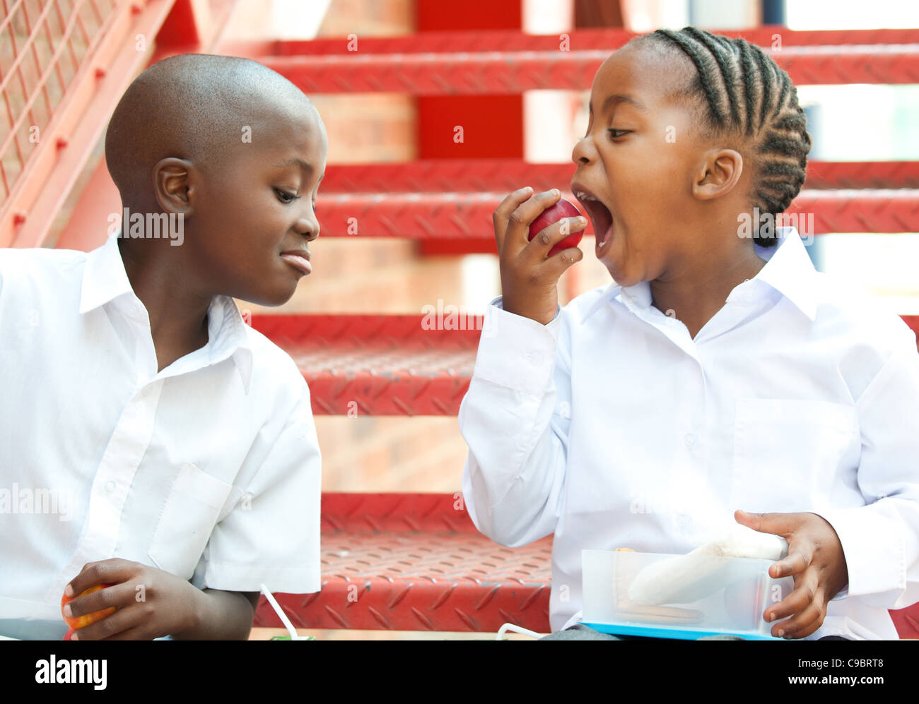 Boy and girl eating apple on steps outside school, Johannesburg ...