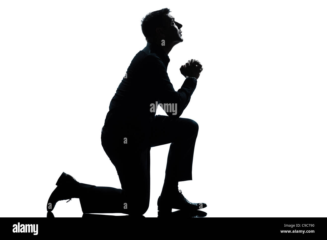 one caucasian man kneeling praying full length silhouette in studio ...