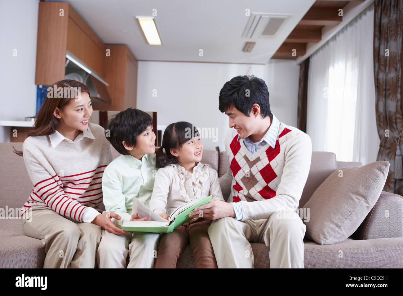 Happy family talking with a book on the sofa Stock Photo - Alamy