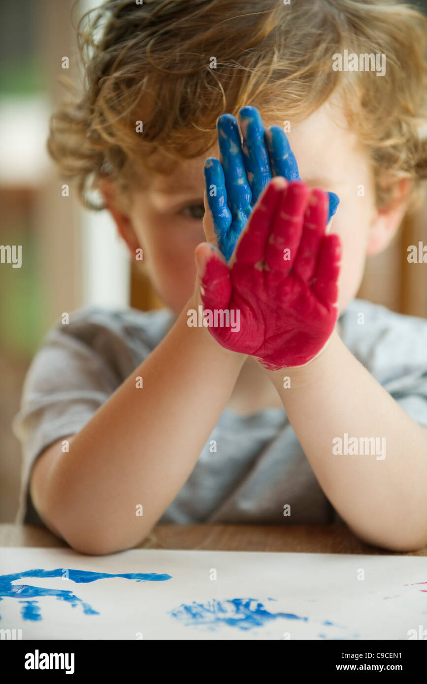 Little boy holding paint covered hands in front of his face Stock Photo ...