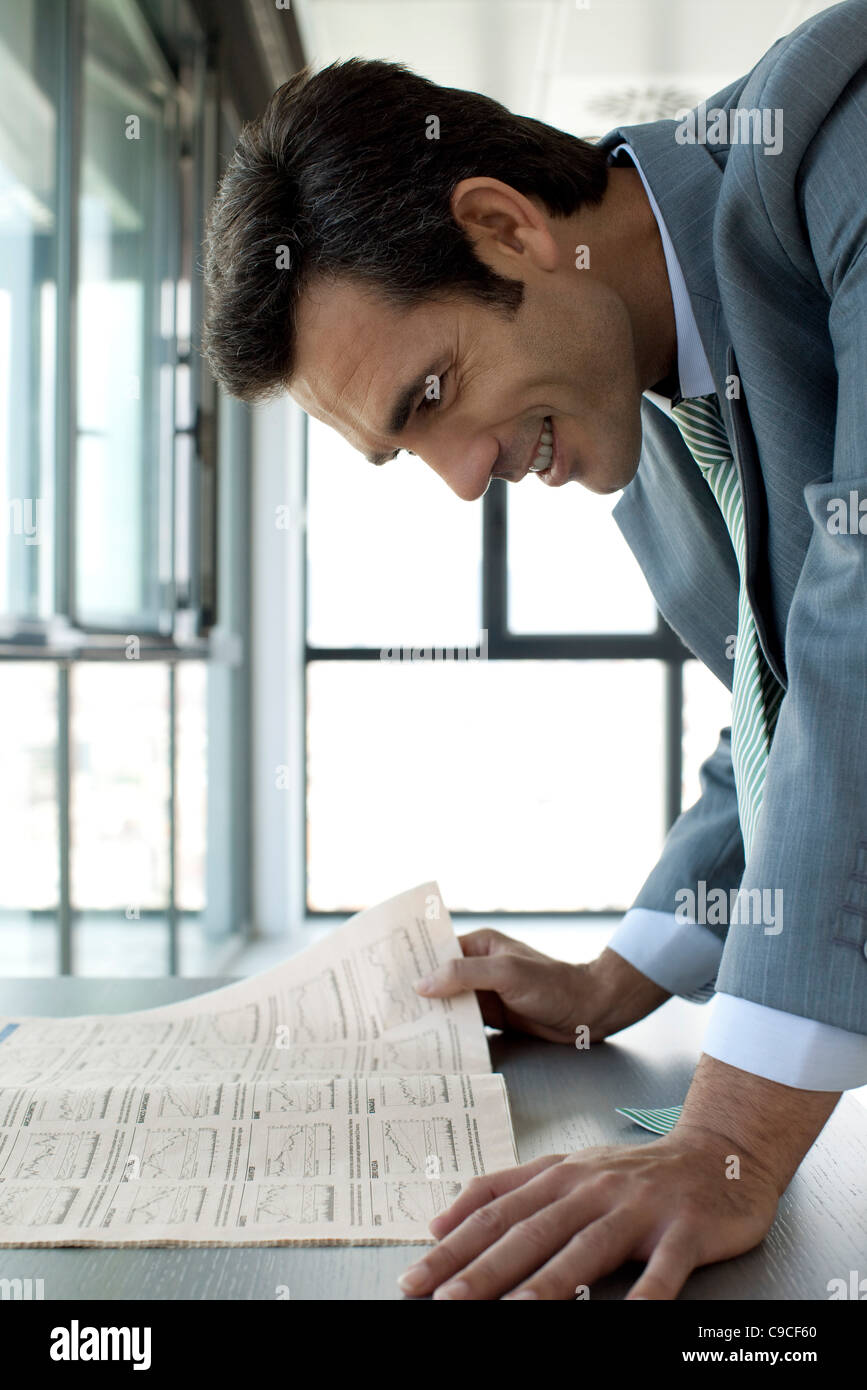Businessman reading finance section of newspaper, smiling Stock Photo ...