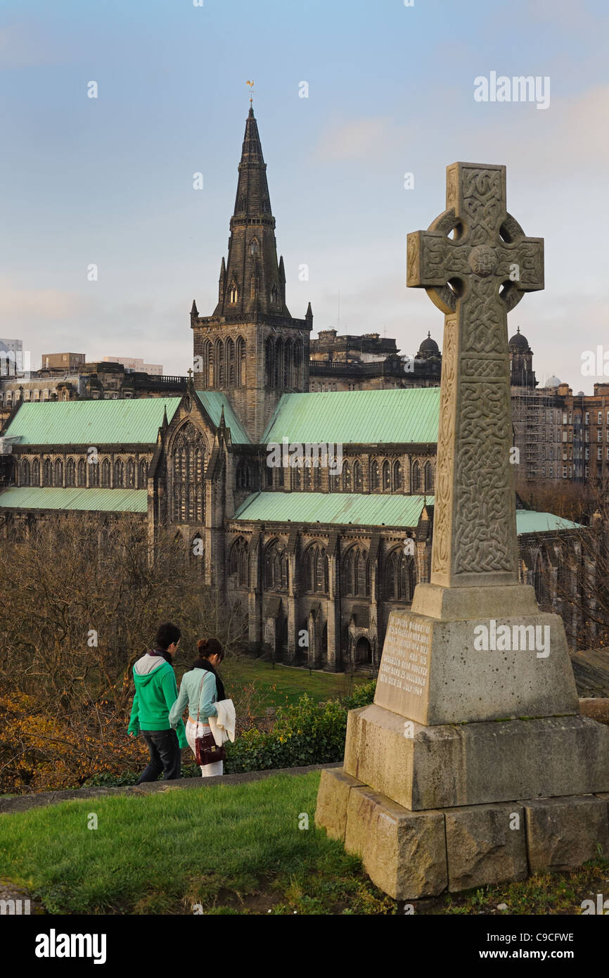 A boy and girl walk past the Celtic cross gravestone in Glasgow ...