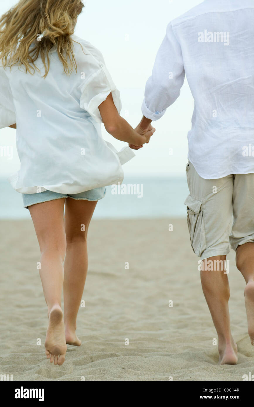 Couple running hand in hand at the beach, rear view Stock Photo - Alamy
