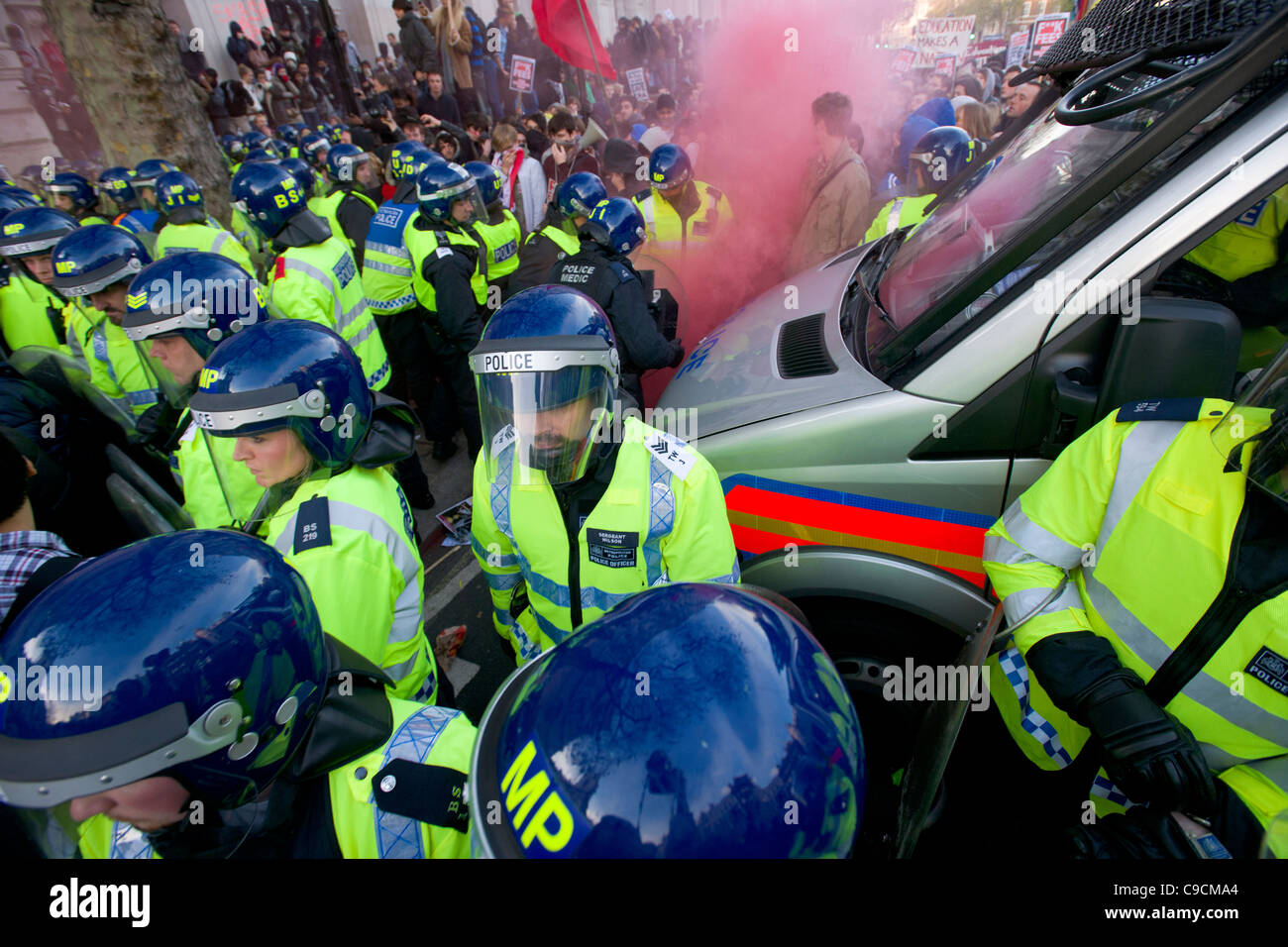 Police in riot gear forming a barrier on Whitehall, bathed in red smoke ...