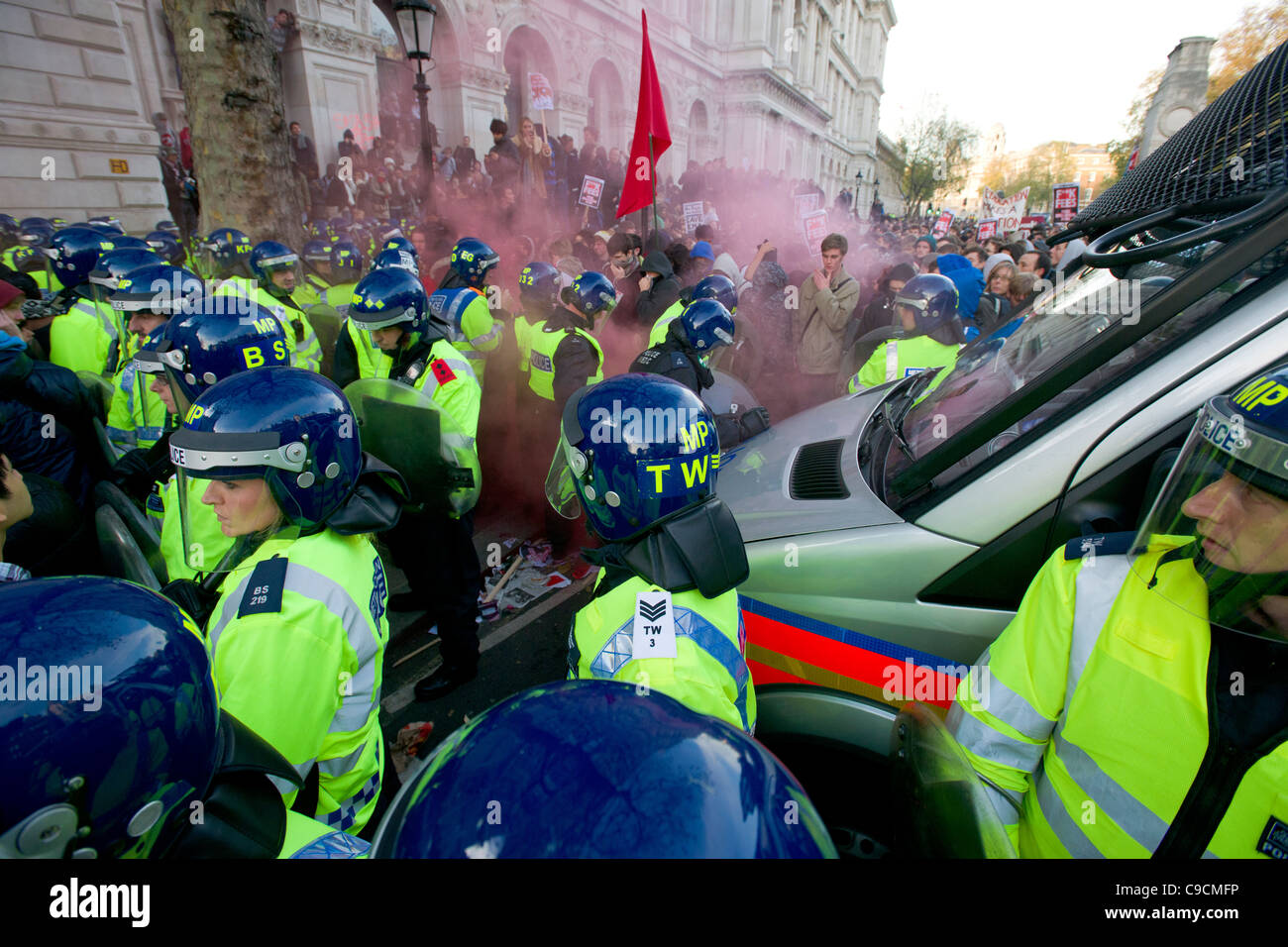 Police in riot gear forming a barrier on Whitehall, bathed in red smoke ...