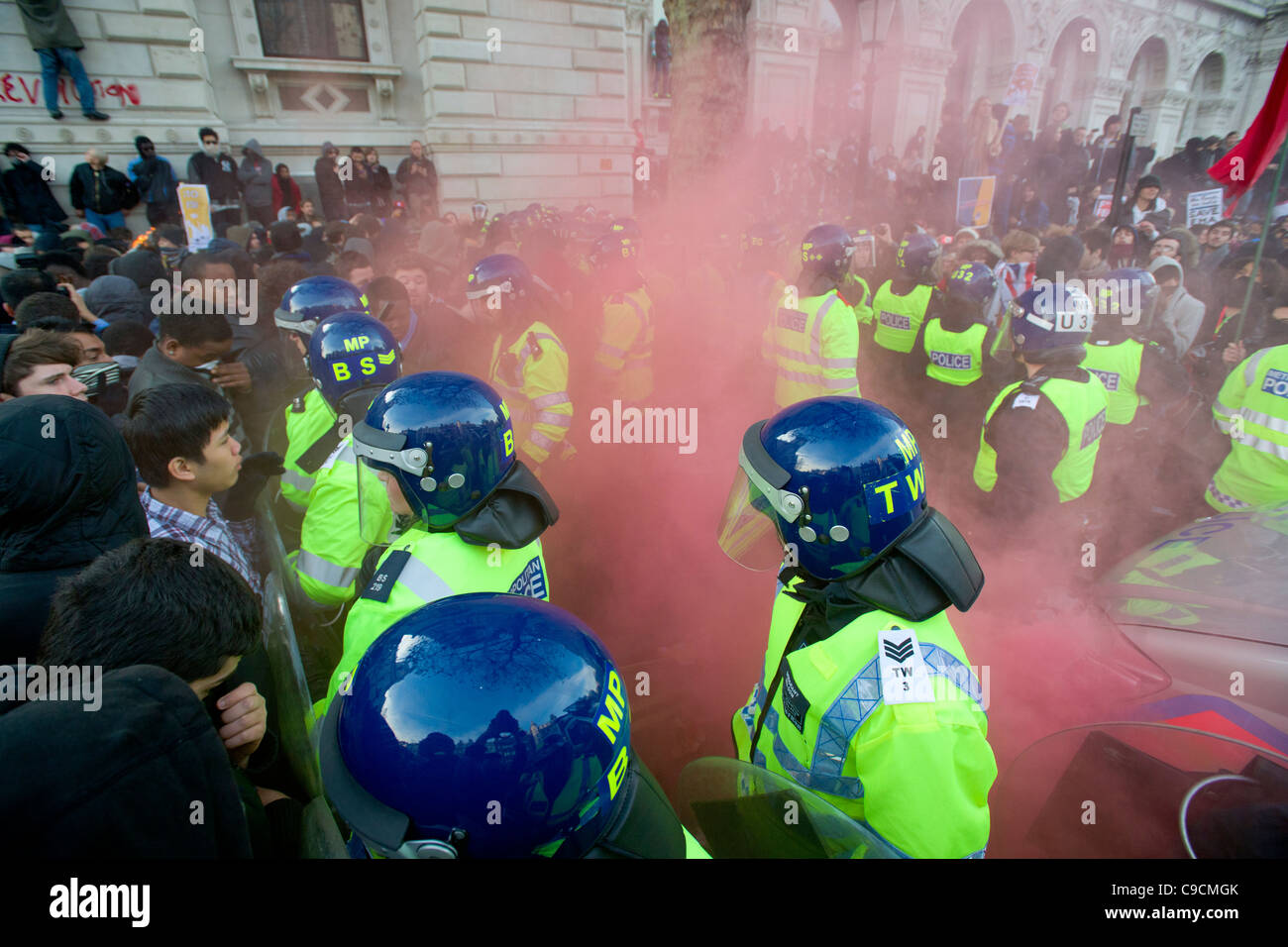 Police in riot gear forming a barrier on Whitehall, bathed in red smoke ...