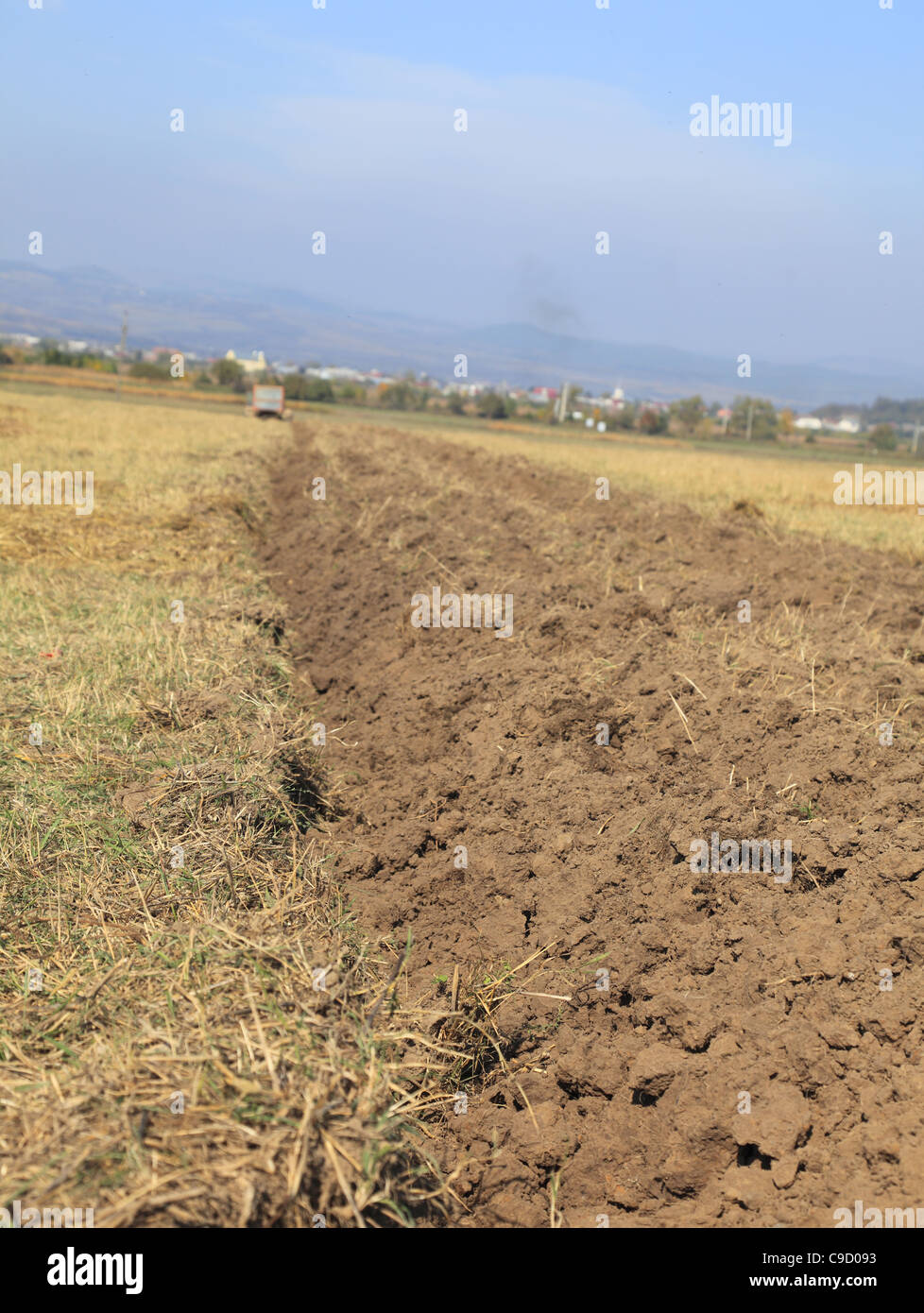 Tilted image of a ploughland with a small tractor in the distance Stock ...