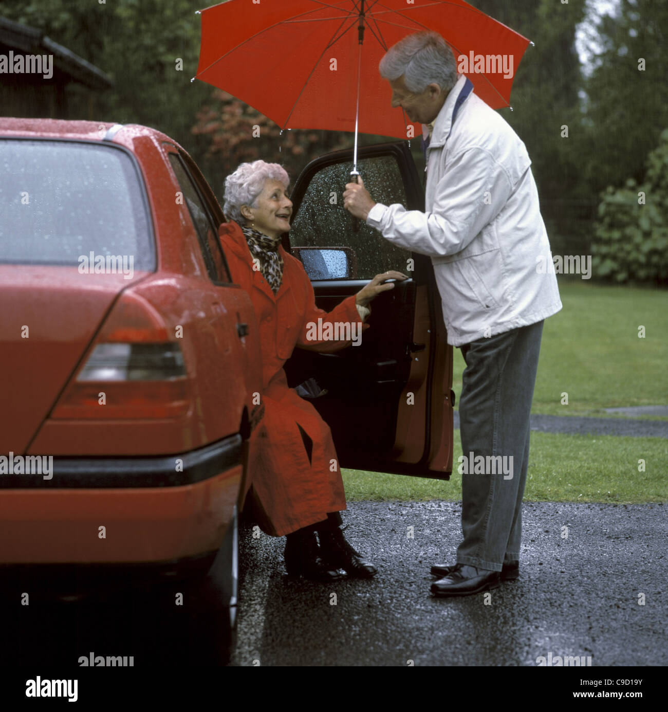 Senior man holding an umbrella above a senior woman exiting a car Stock ...