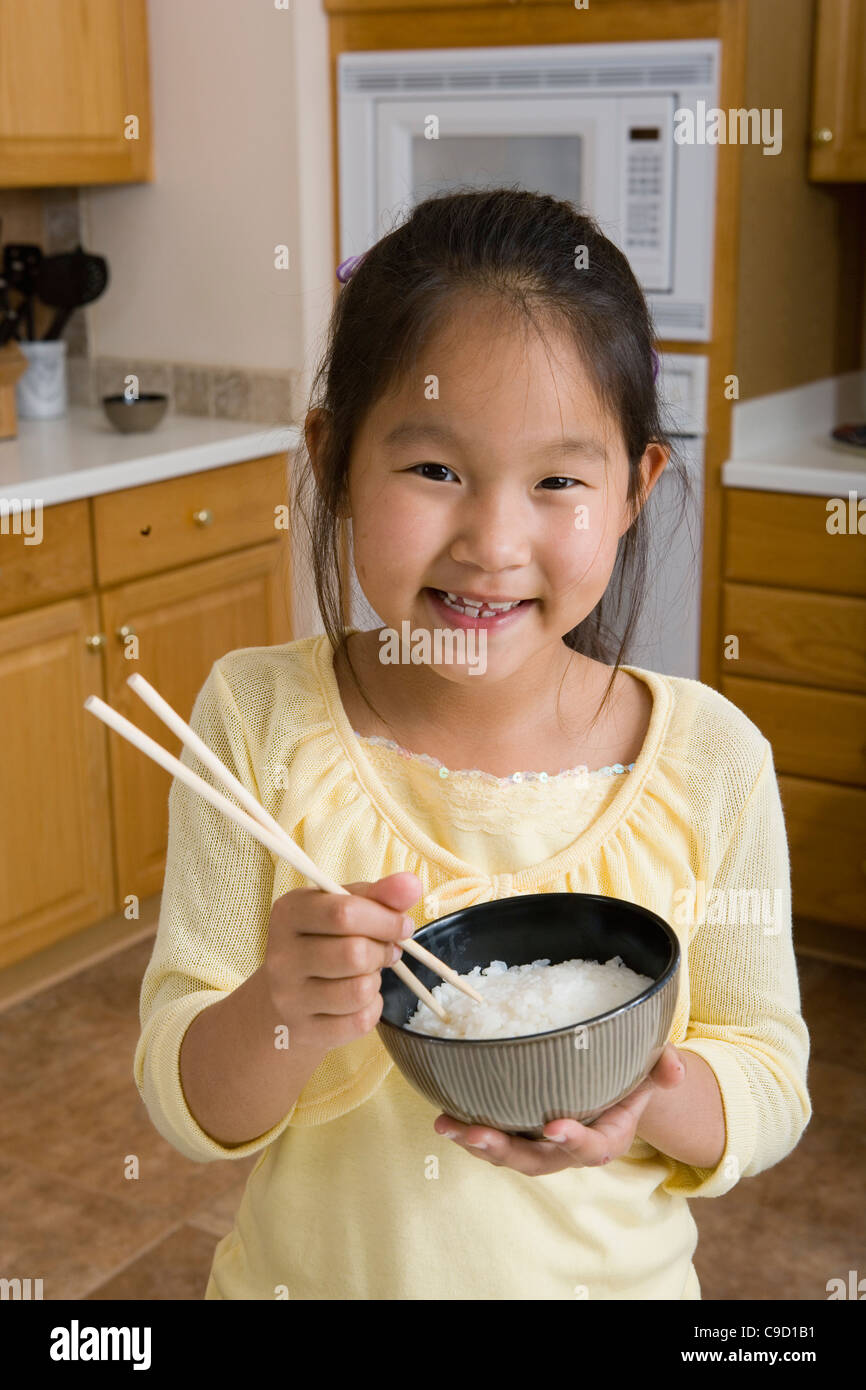 Portrait of an Asian girl in kitchen holding bowl of rice and ...