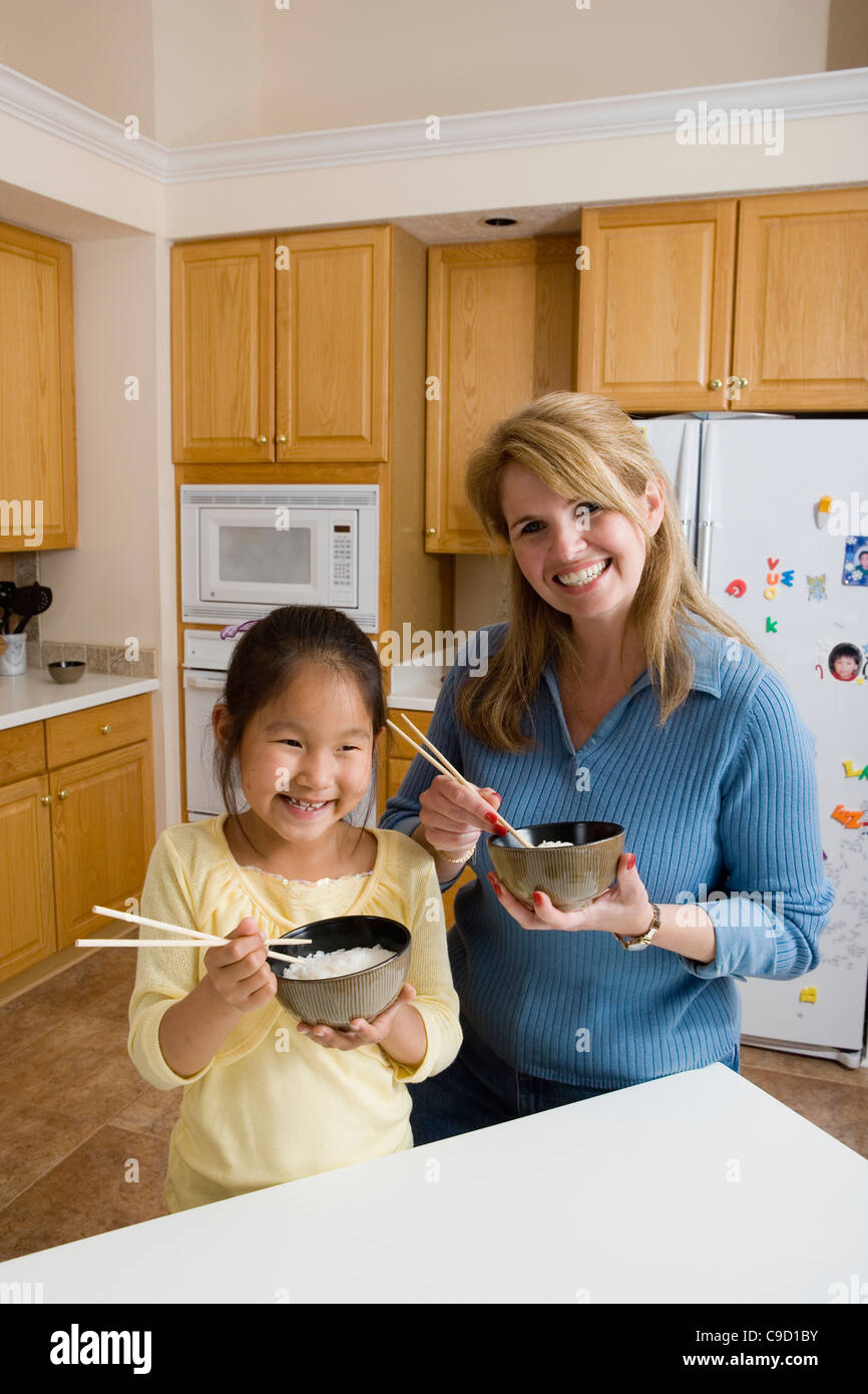 Portrait of mother and daughter in kitchen holding bowls of rice and ...
