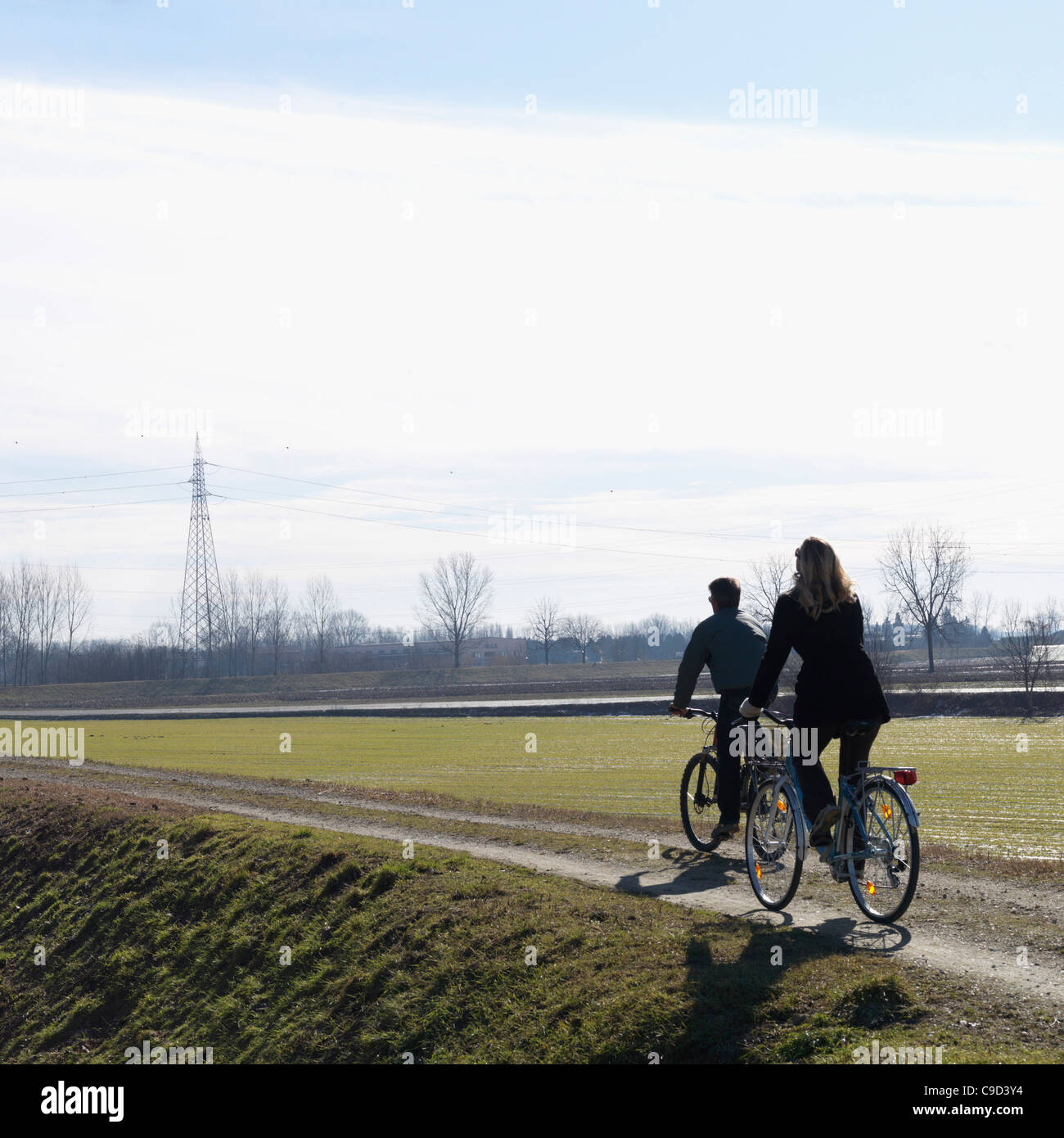 Italy, Couple bike along raised dike above field, power pylons Stock ...