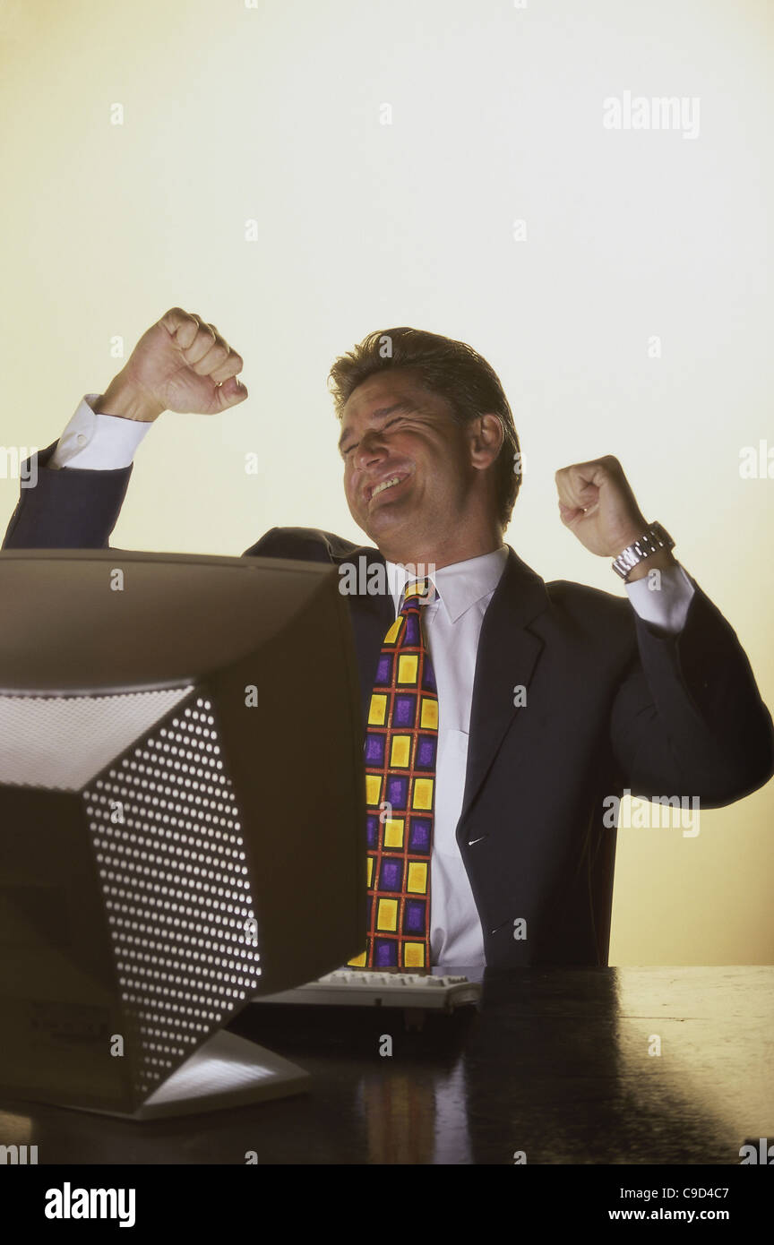Businessman sitting in front of a computer with his hands raised Stock ...