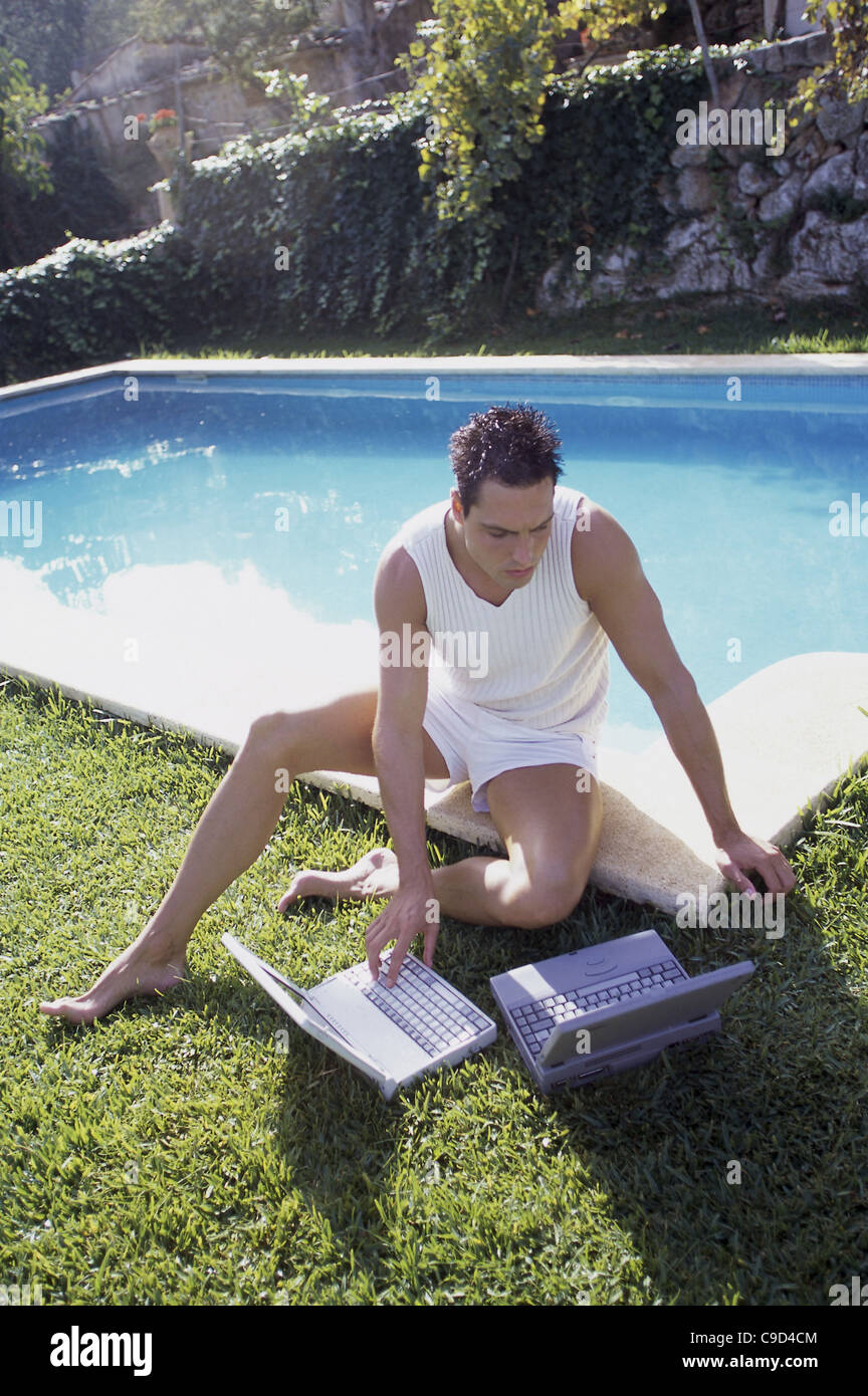 Young man sitting beside a swimming pool using a laptop Stock Photo - Alamy