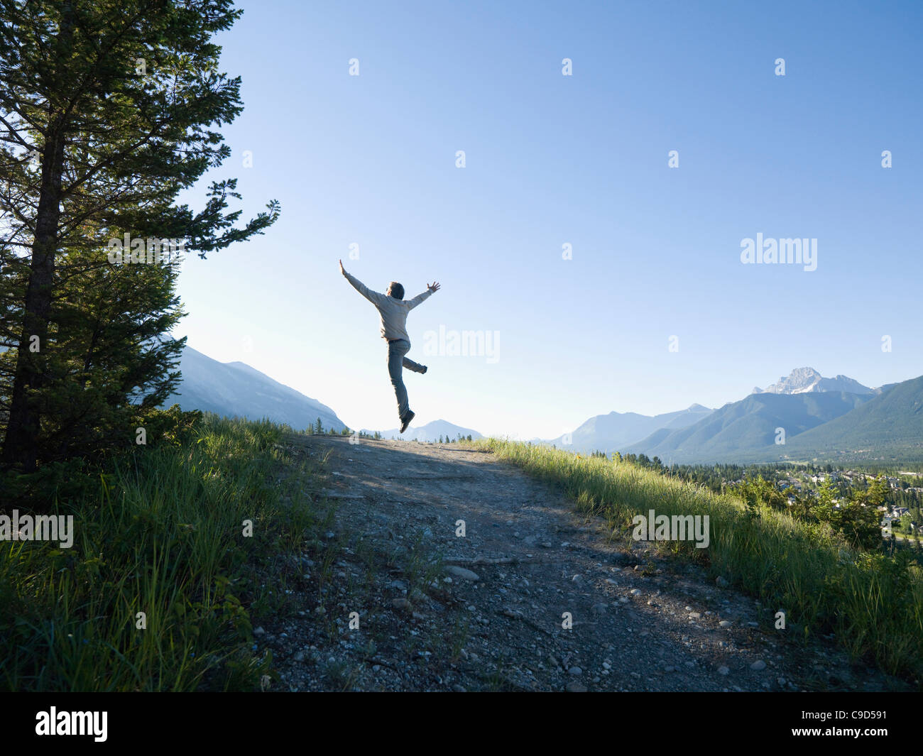 Canada, Alberta, Canmore, Rear view of man jumping above mountain trail ...