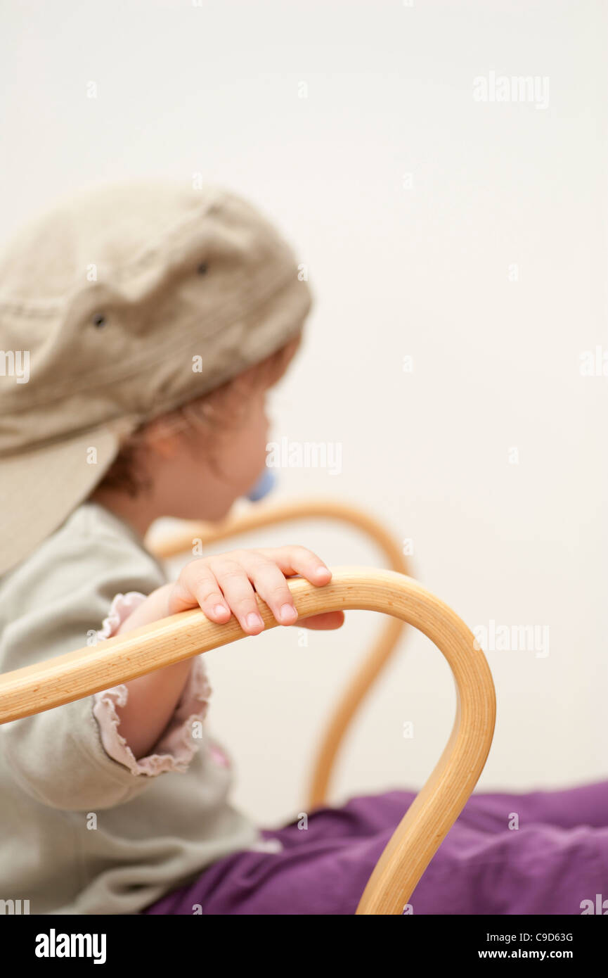 Baby girl with cap, sitting in chair Stock Photo - Alamy