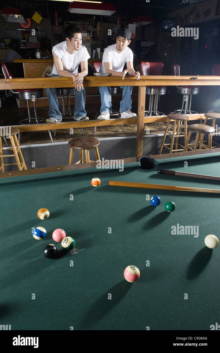 Portrait of two men in jeans and t-shirts sitting in front of billiards ...