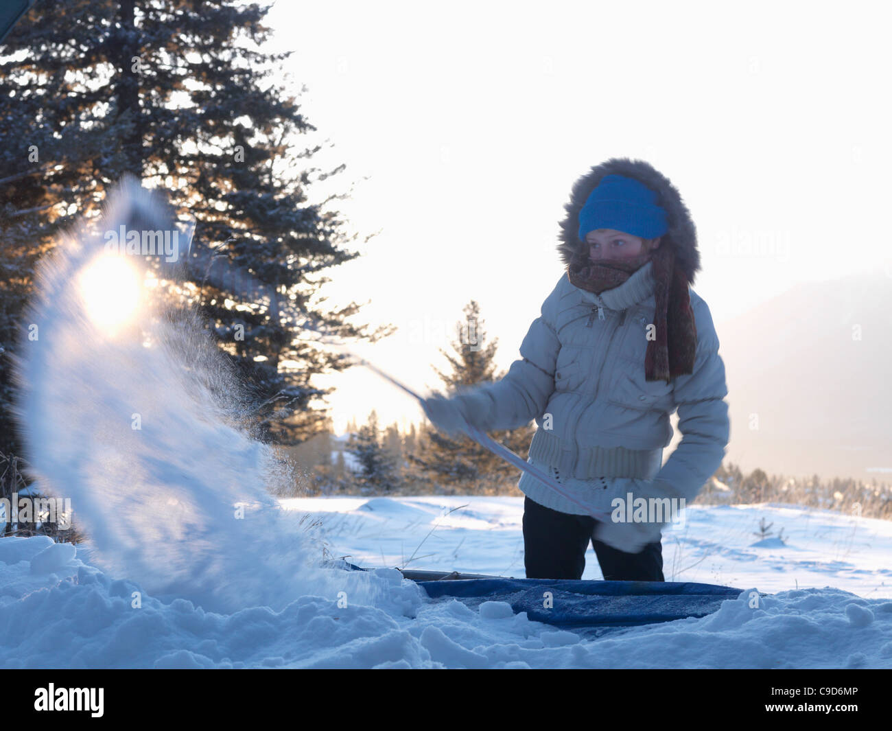 Canada, Alberta, Teenage girl brushing deep snow off trampoline, cold ...