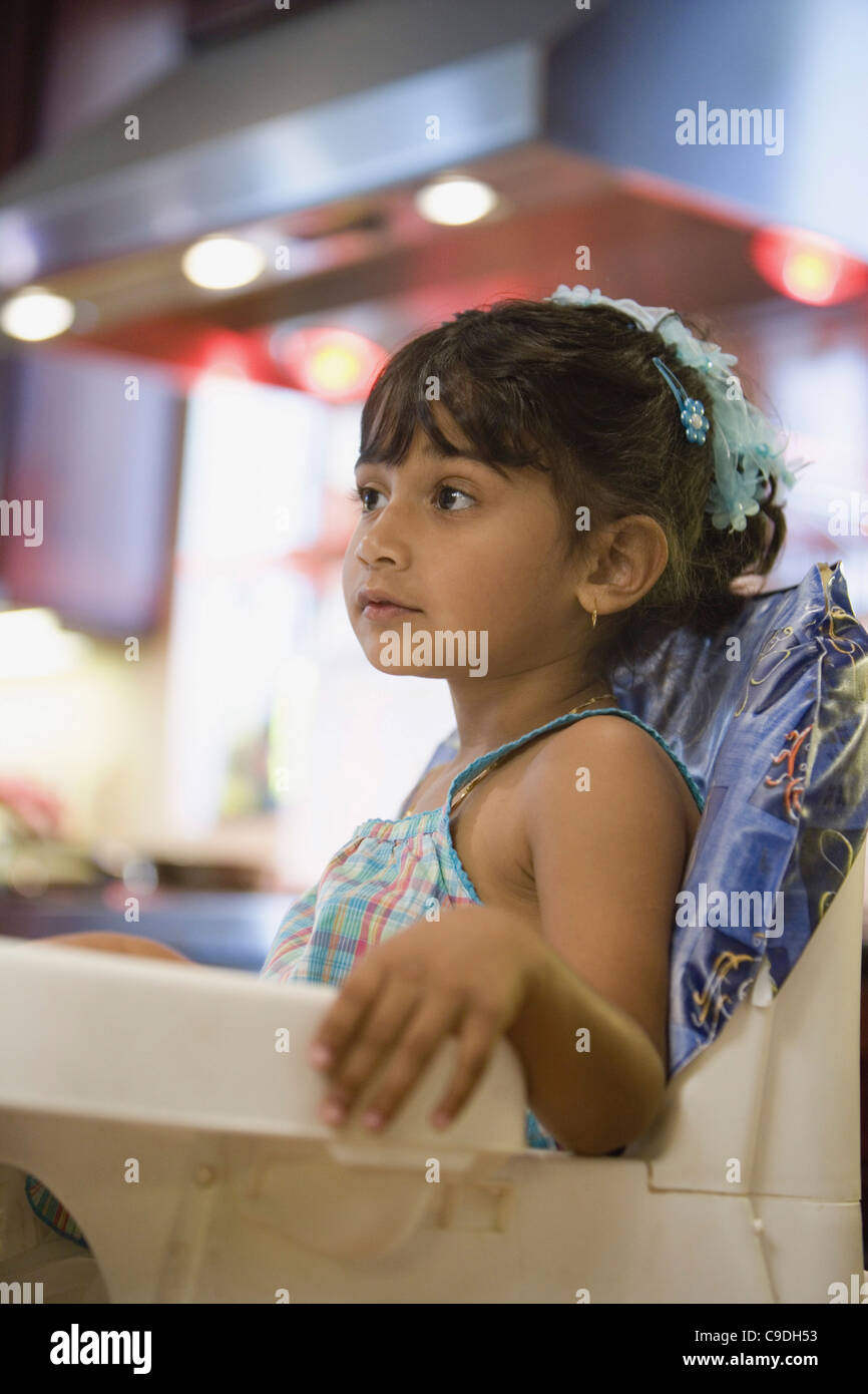 Side view of a young girl sitting on a high chair Stock Photo - Alamy
