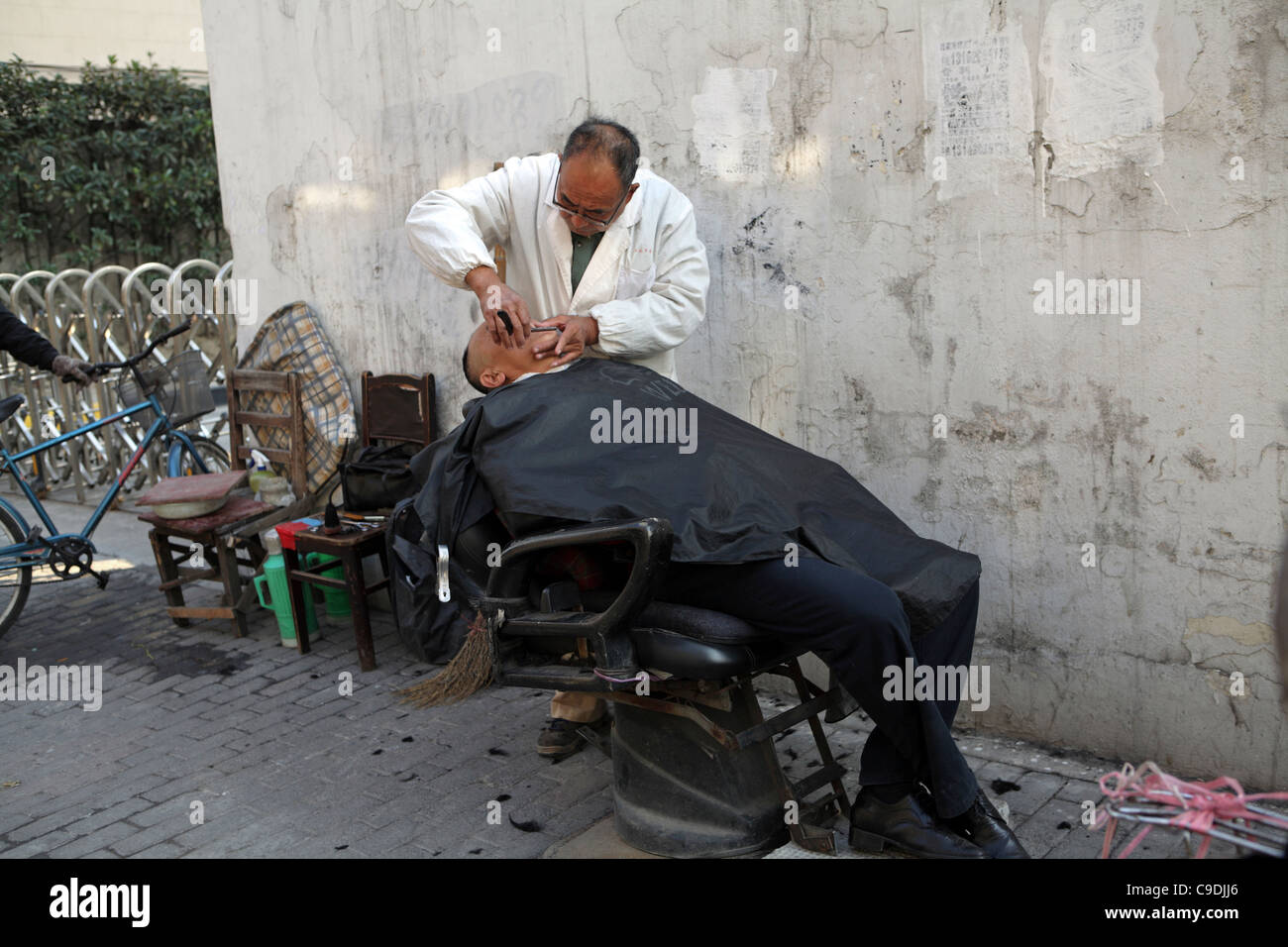 Barber giving client a shave outside on pavement, street market ...