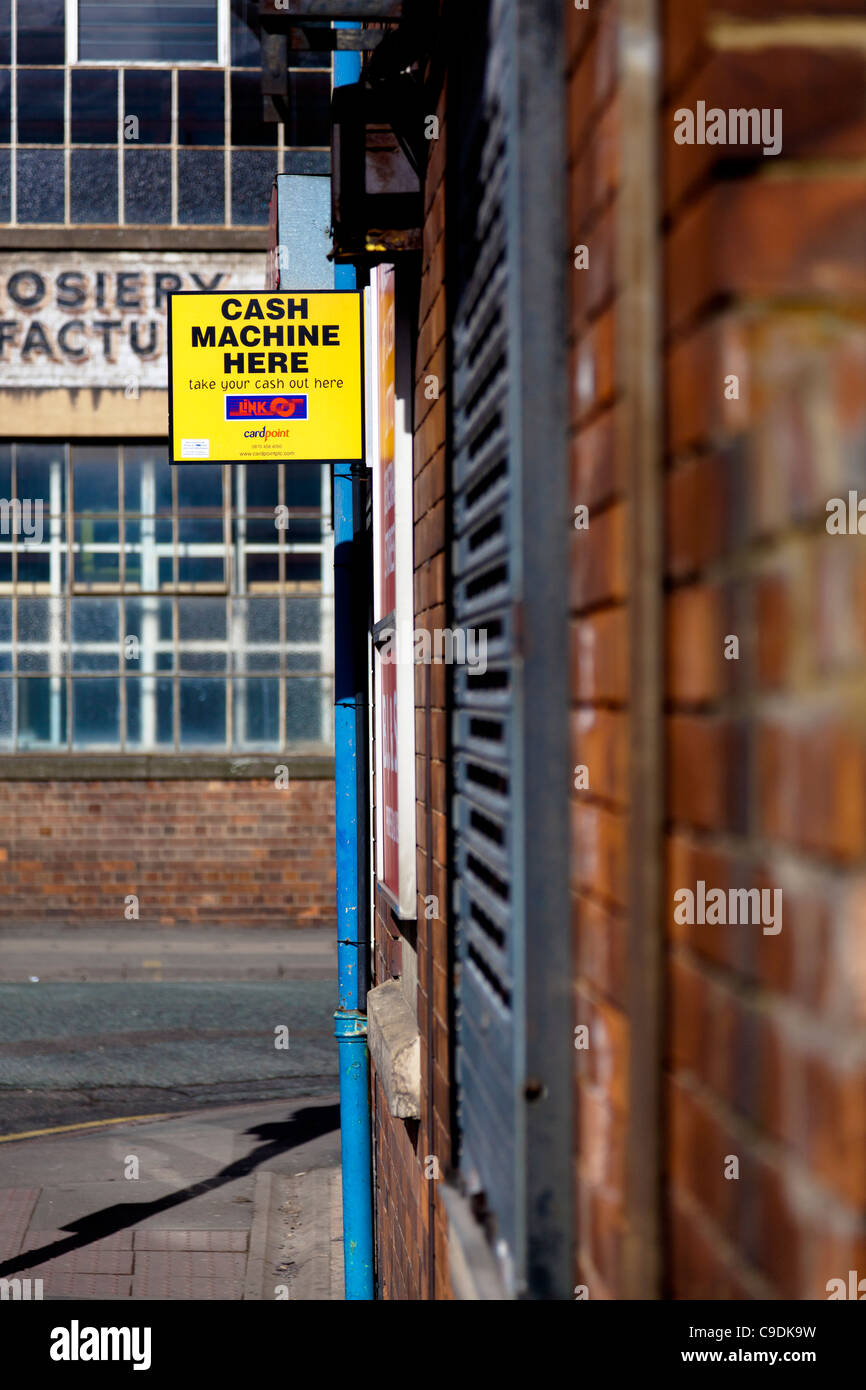 Bright yellow cash machine sign contrasted against an old manufacturing ...