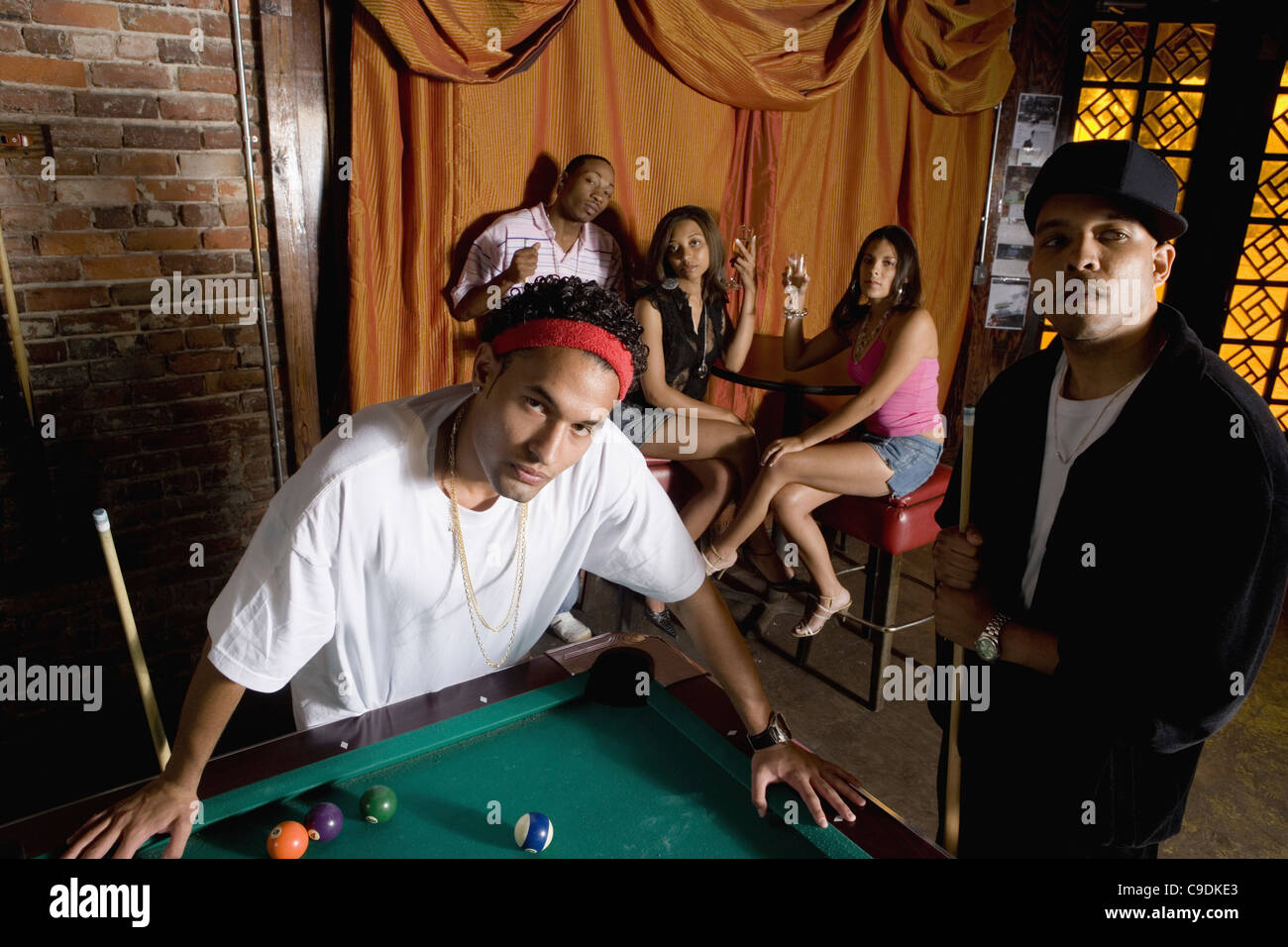 Portrait of young men in hip-hop fashion leaning against pool table ...