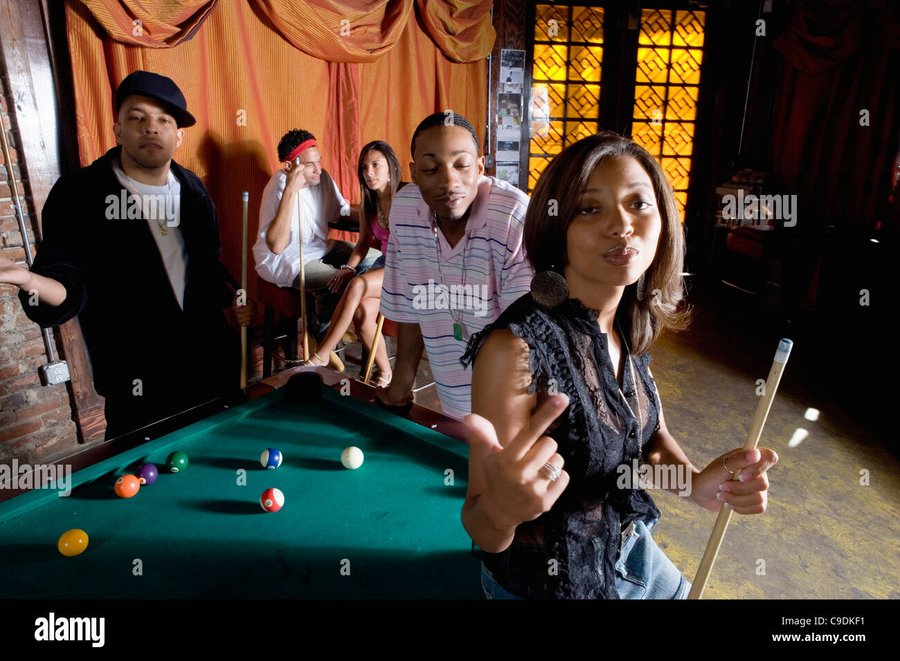 Young woman with pool stick next to pool table with friends watching in ...
