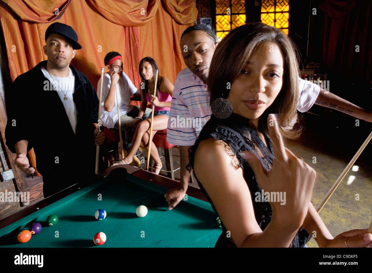 Young woman with pool stick next to pool table with friends watching in ...