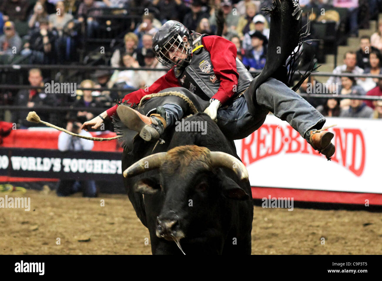 A helmet-wearing cowboy tries to hang onto the rope while riding a bull ...