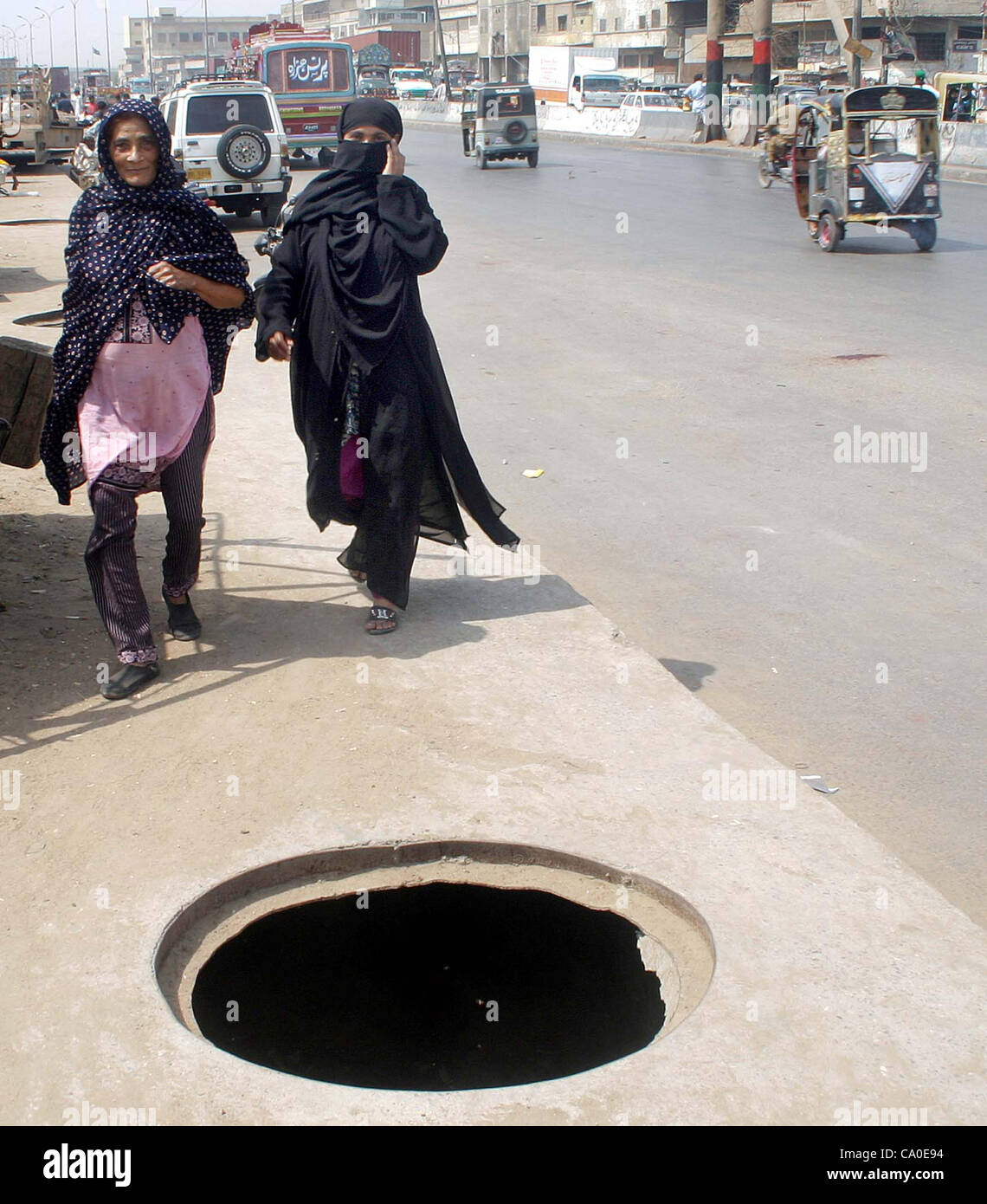 Two women pass through at an open mainhole on footpath at a road which ...