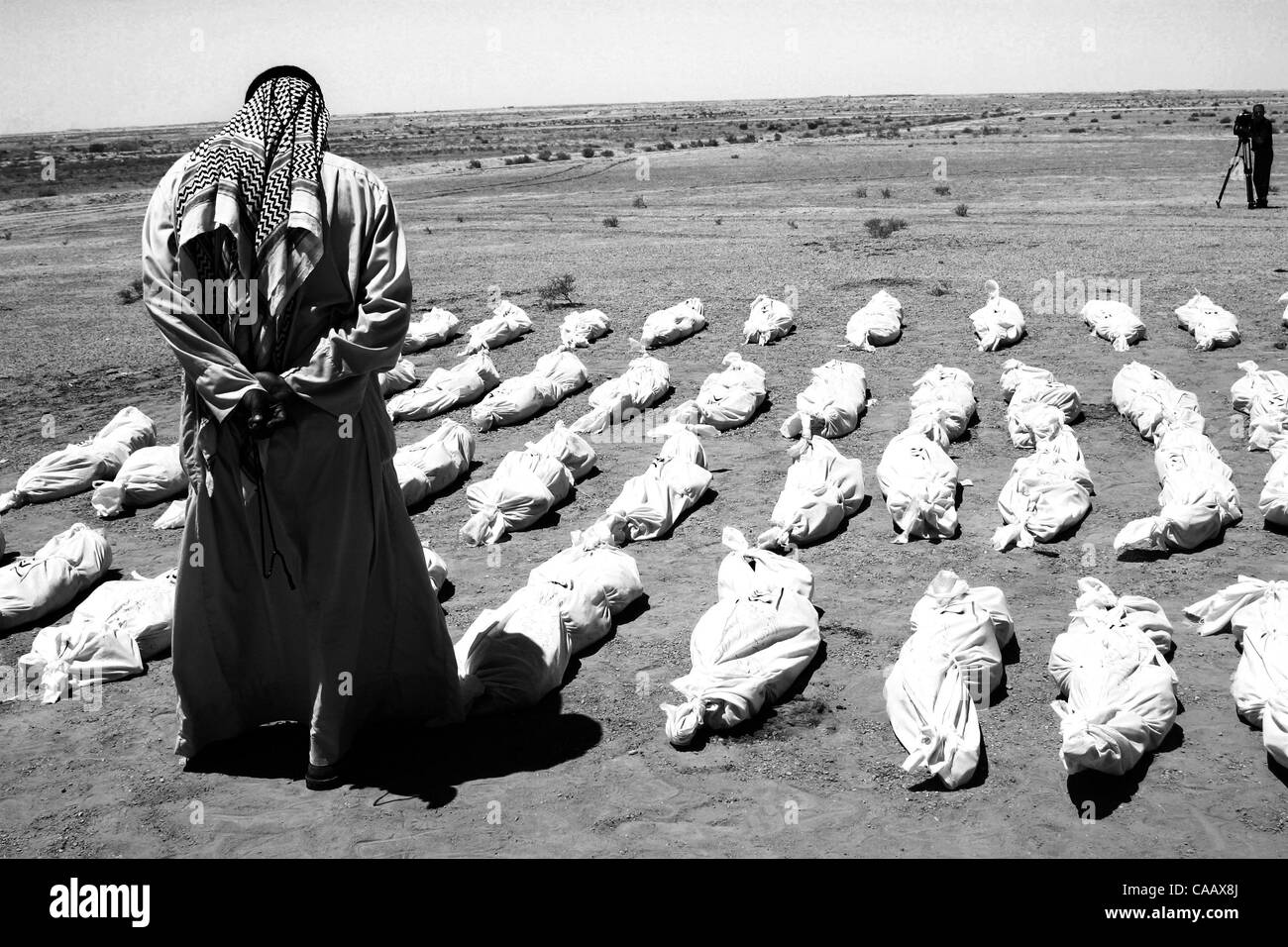 An array of shroud-wrapped remains lie in the desert at a mass grave ...