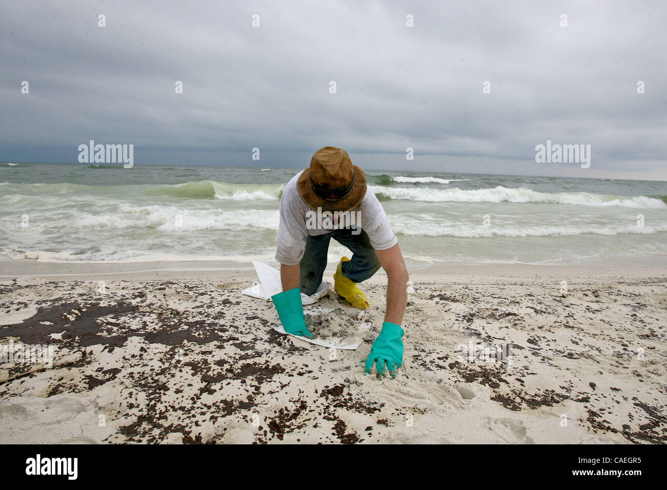 A member of a clean up crew scoops up oil that has washed ashore at the ...