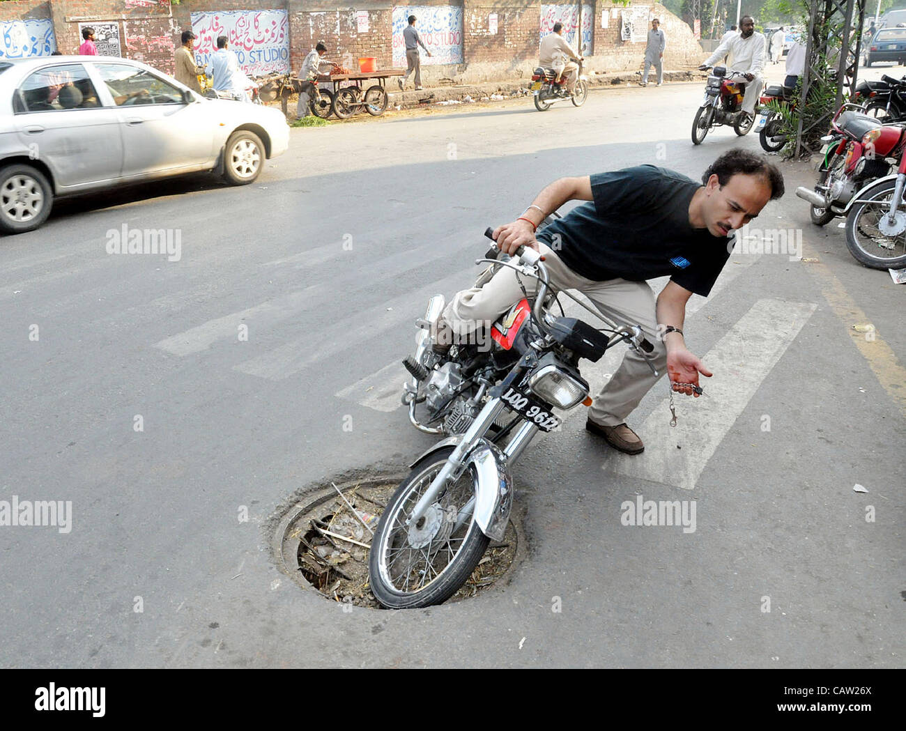 A motorcyclist loses his balance due to an open mainhole showing the ...