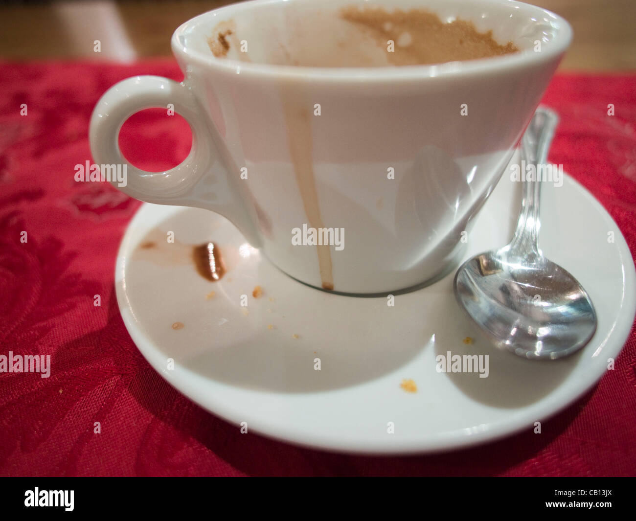 An almost empty coffee cup sits on a saucer with an accompanying spoon ...